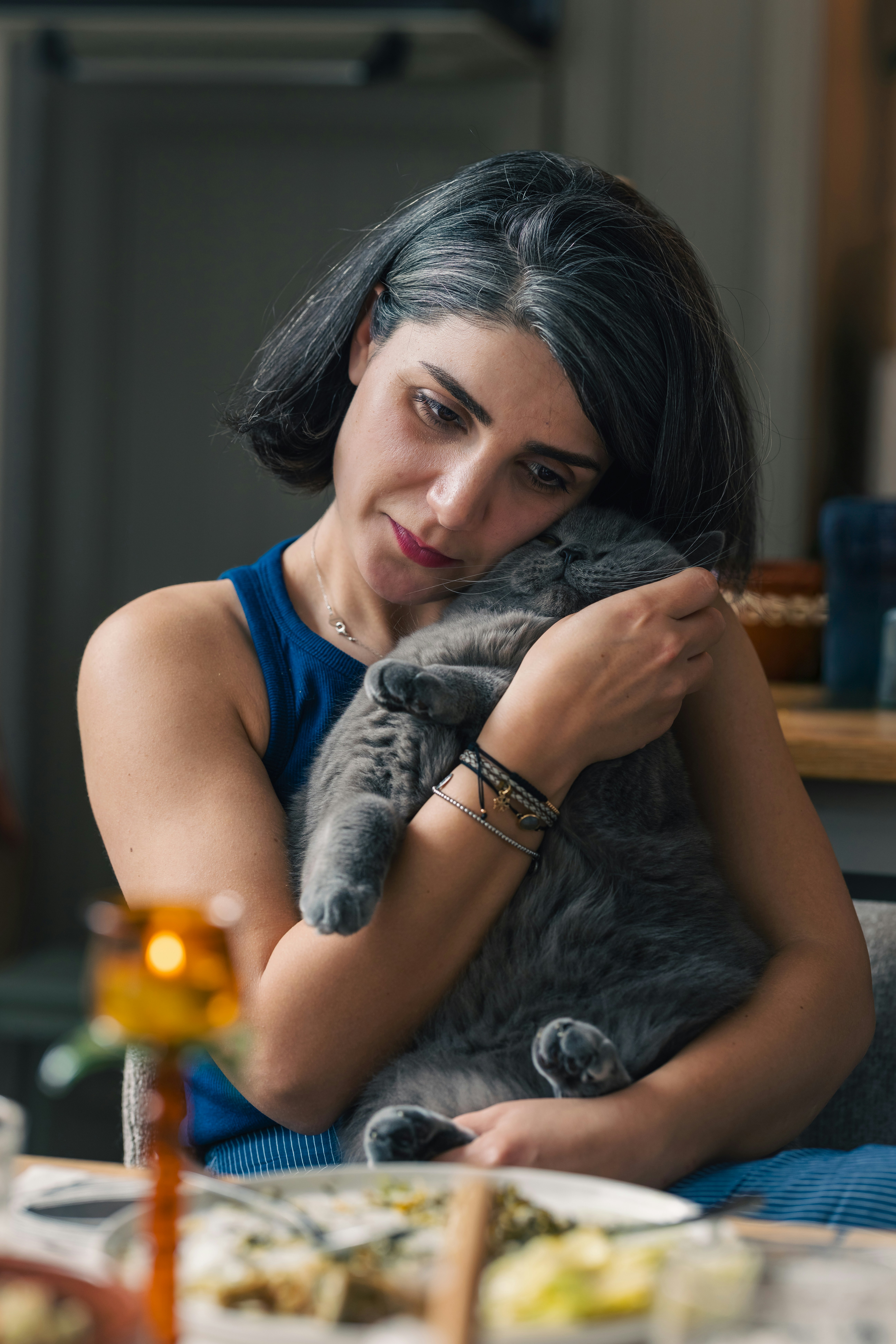 Soft Embrace: A Woman and Her Grey Cat Share a Quiet Table Moment