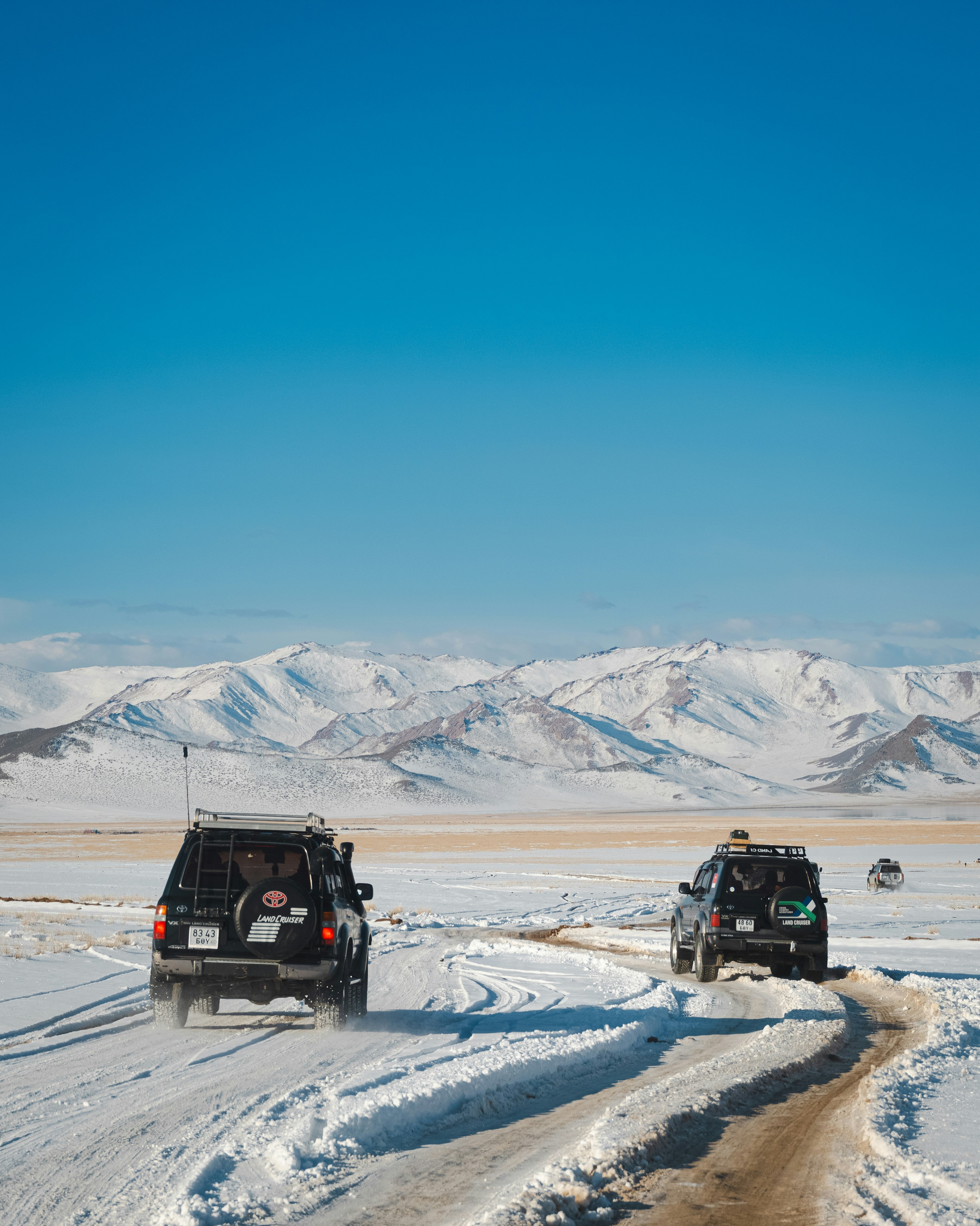 Snowbound Crossroads: Twin 4x4s carving a frozen ribbon toward distant peaks