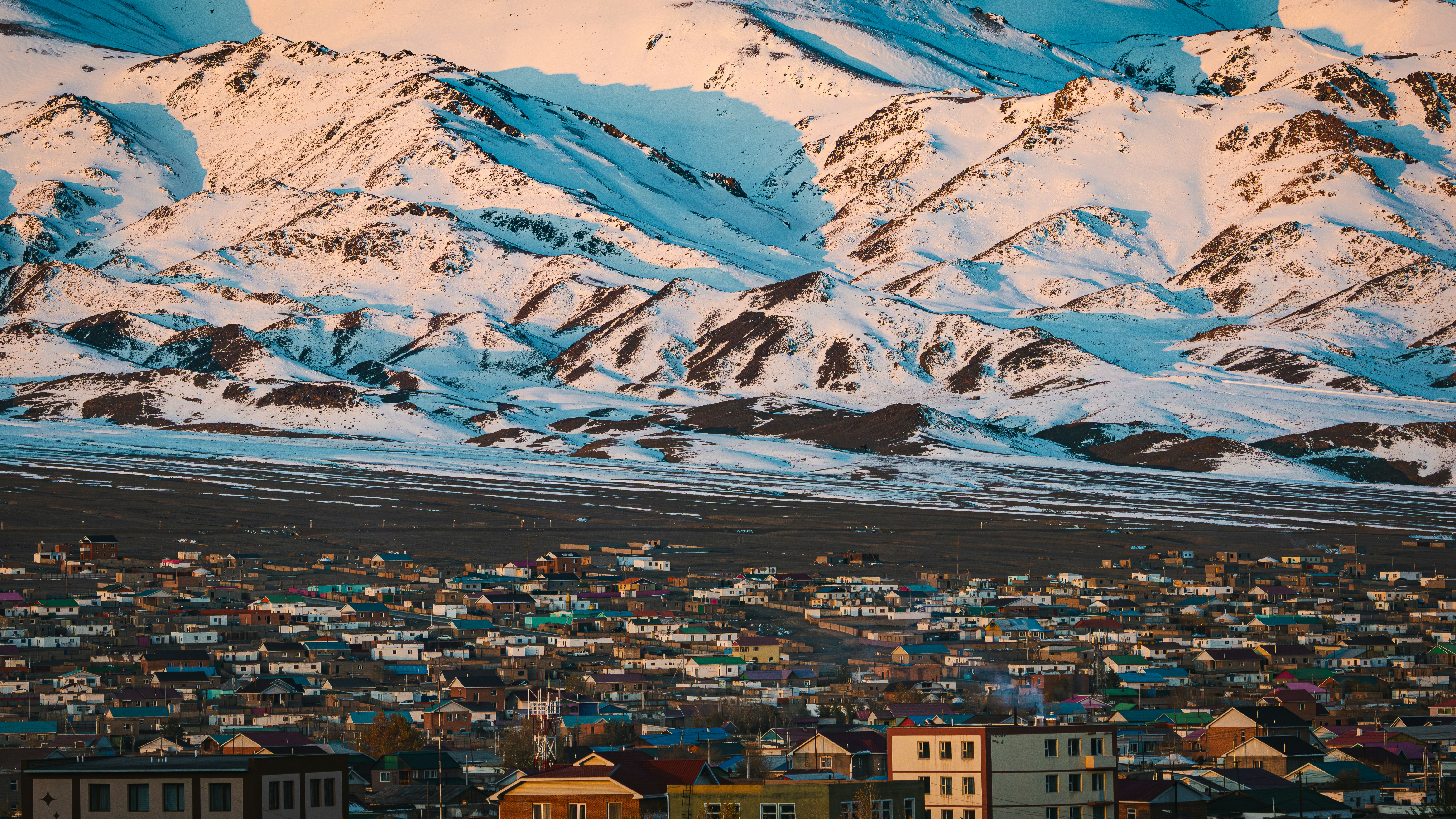 Multicolored town sprawled across a plain with snow-dusted mountains looming in the background.