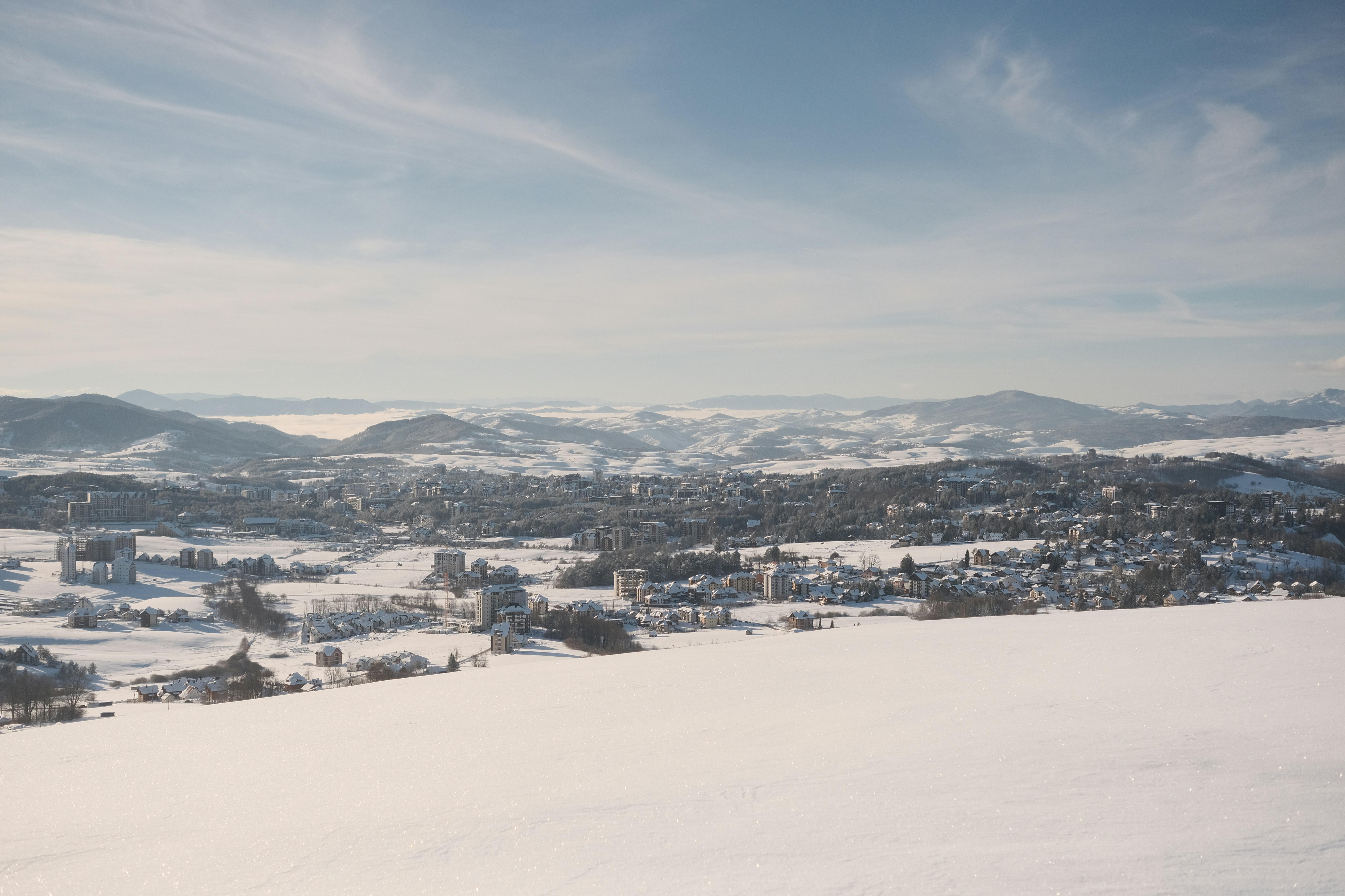 Snow-covered town nestled among rolling hills under a clear blue sky.