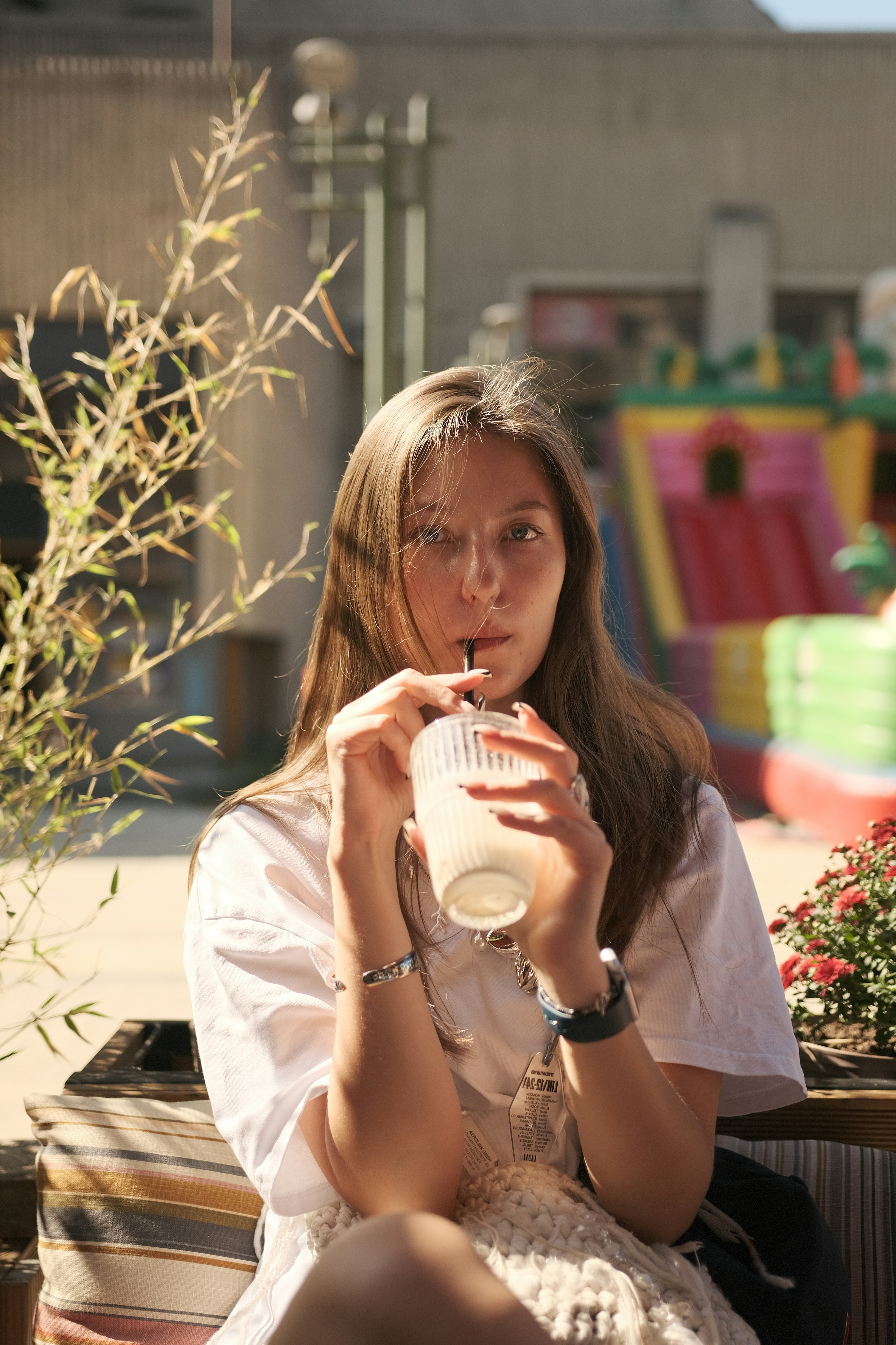 Sunlit Sip at the Playground: A Portrait Beside a Colorful Inflatable Backdrop