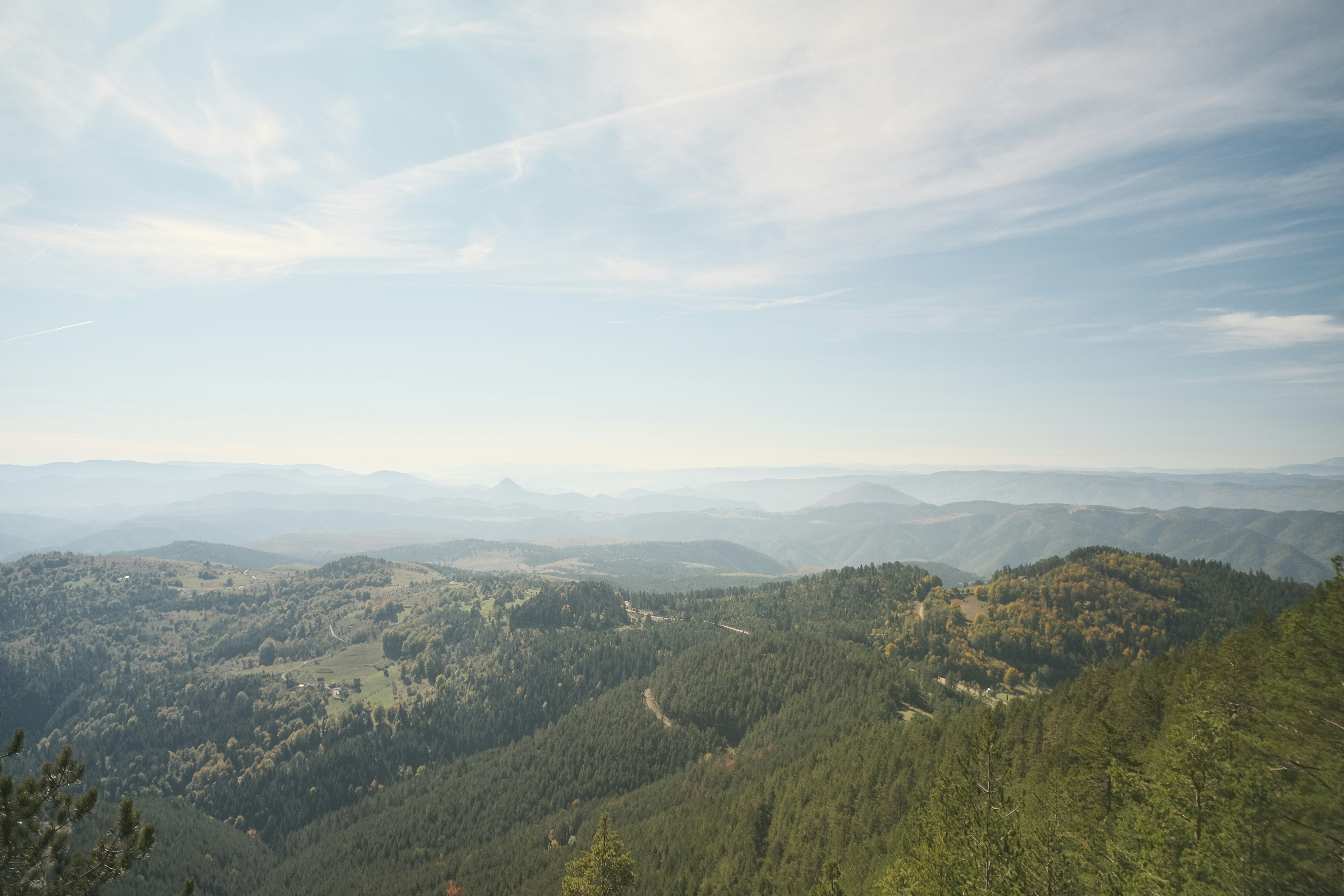 Expansive green hills stretch under a soft blue sky with wispy clouds.