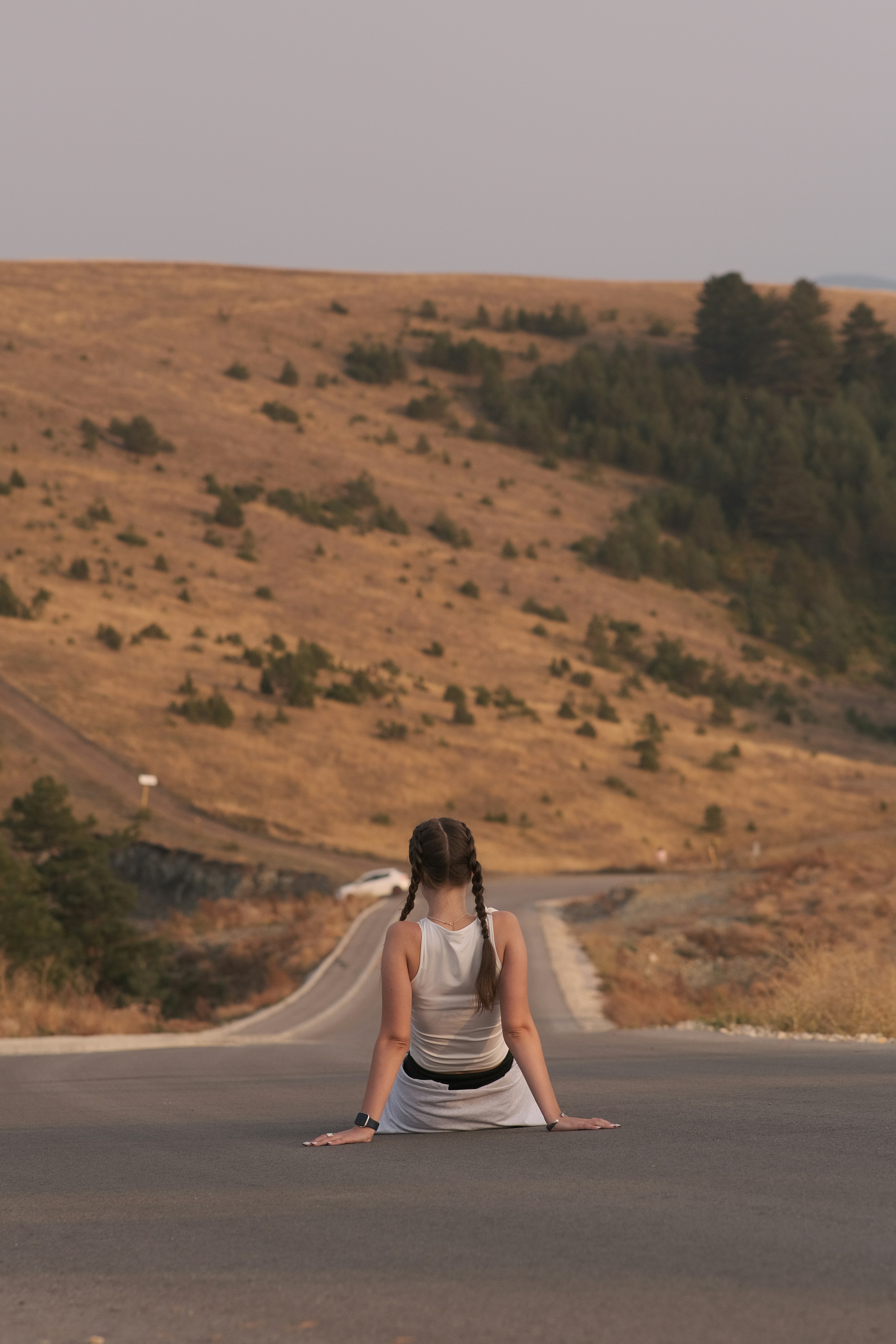 A person sitting on a deserted road, surrounded by a vast landscape of dry hills and sparse trees, evoking a sense of solitude and contemplation.