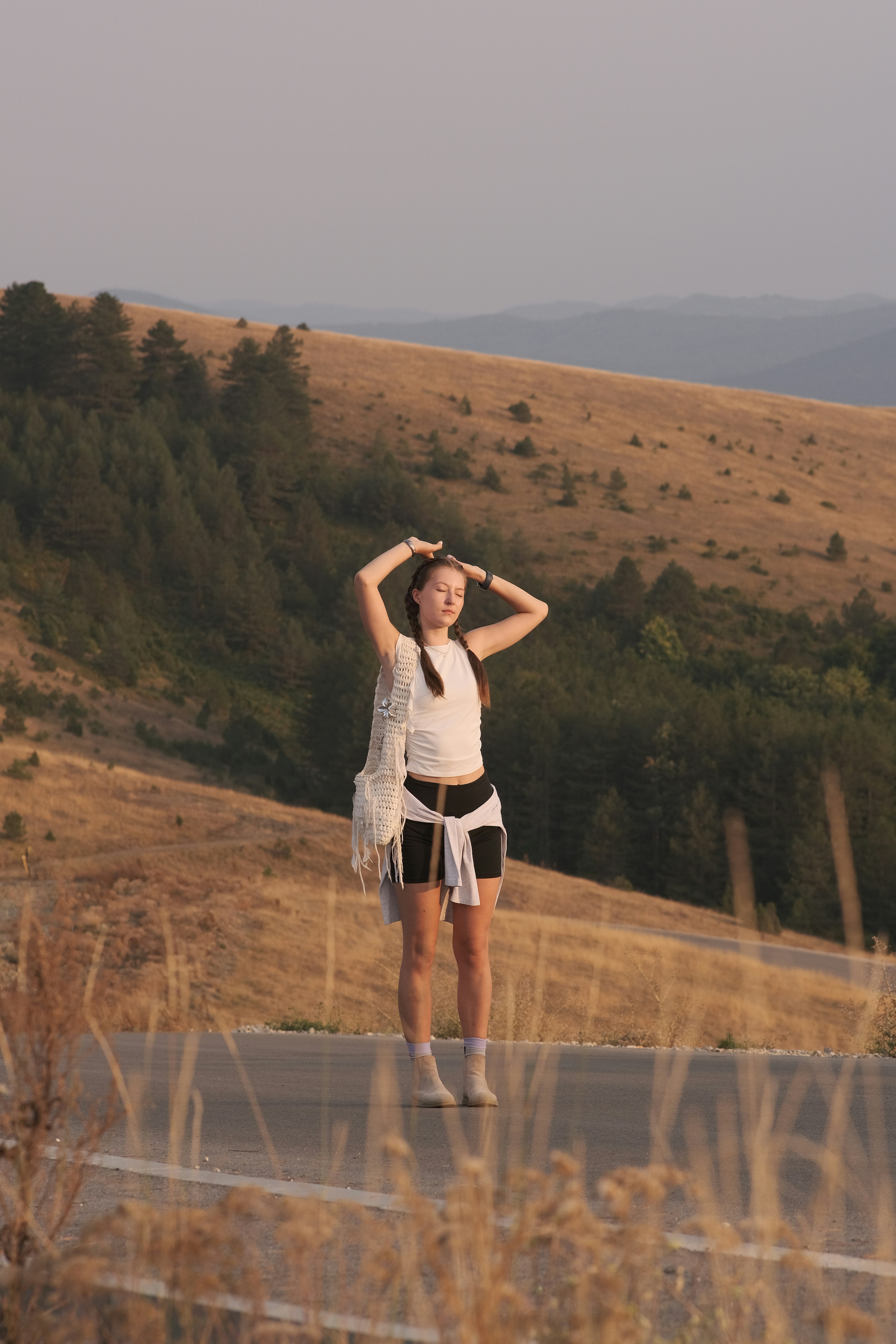 Golden Hour Solitude on a Hill Road: A Girl Poses Amid Rolling Pines