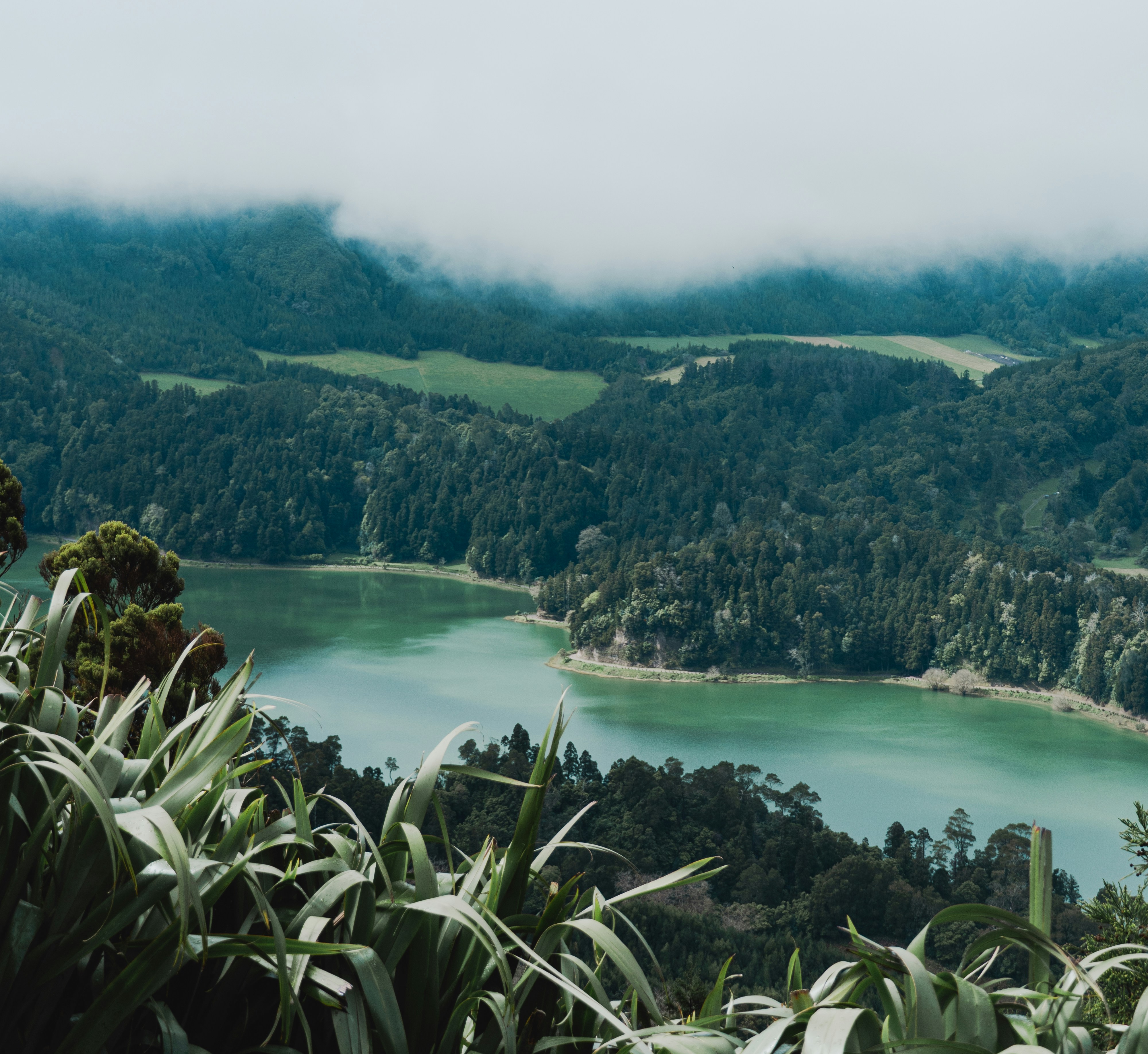 Lush green landscape surrounding a tranquil lake, partially shrouded by misty clouds in the background.