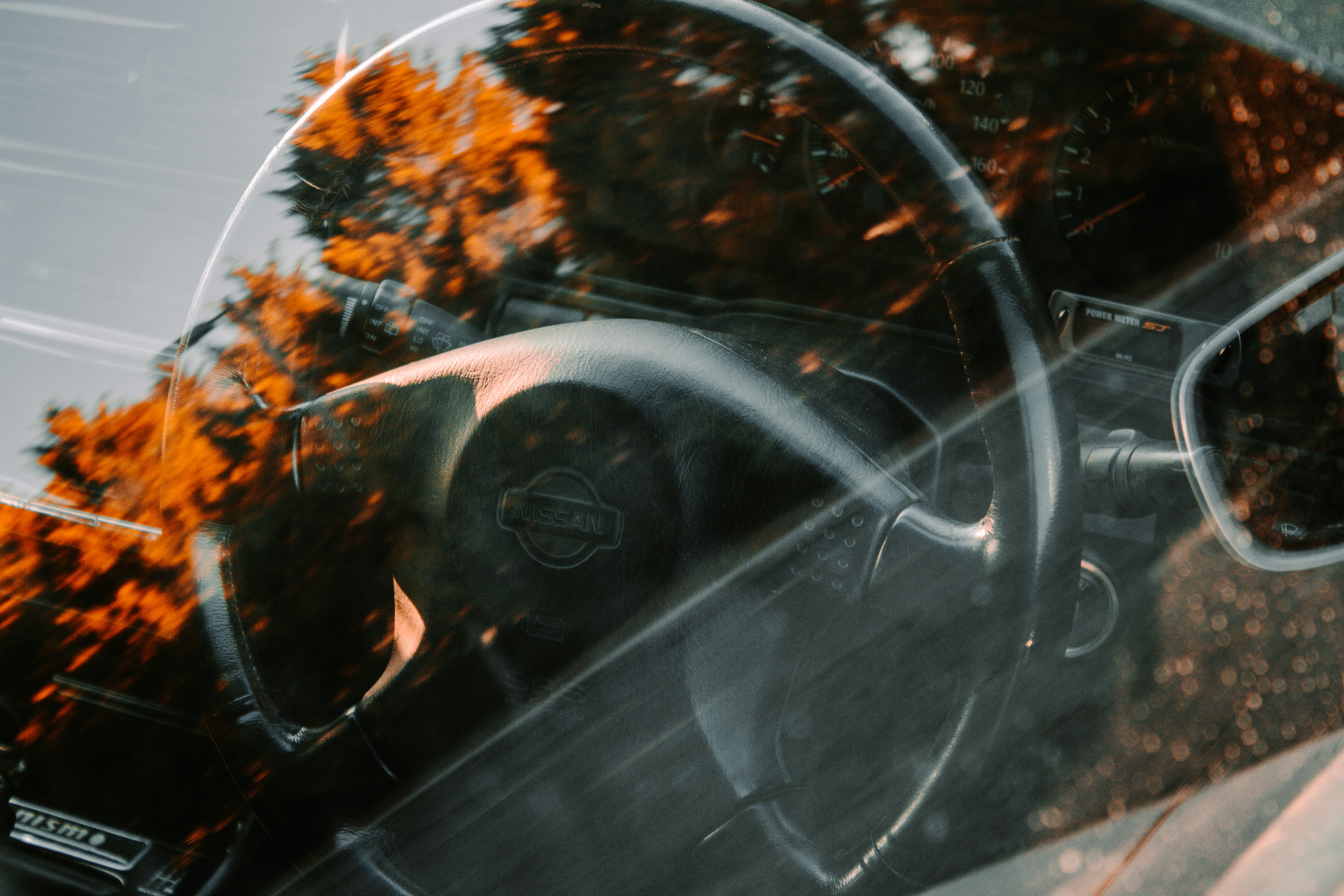 Reflection of autumn foliage on a car windshield, blending seamlessly with the interior view of a steering wheel.