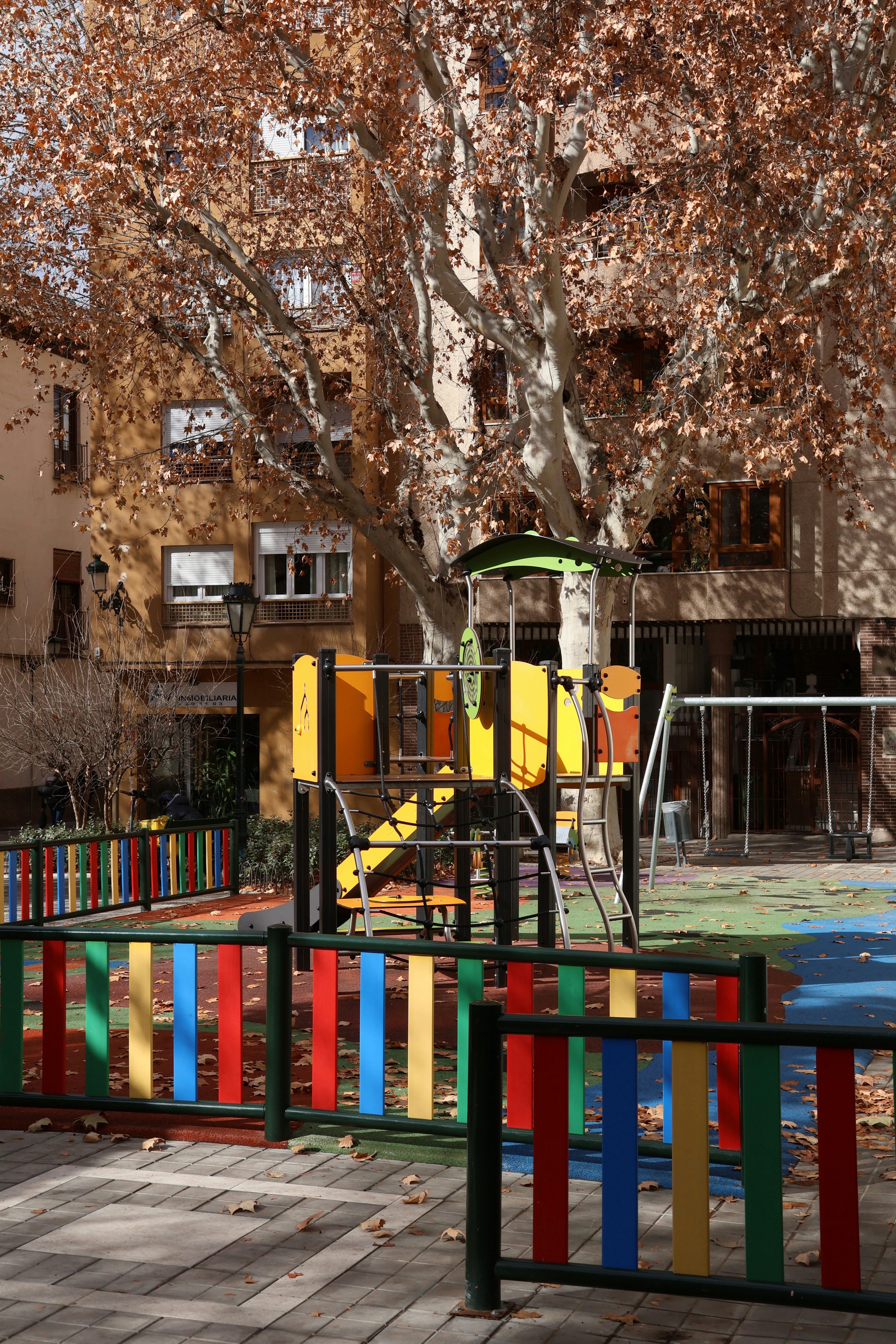 Colorful playground equipment surrounded by vibrant fall foliage and residential buildings. A serene urban play area invites exploration.