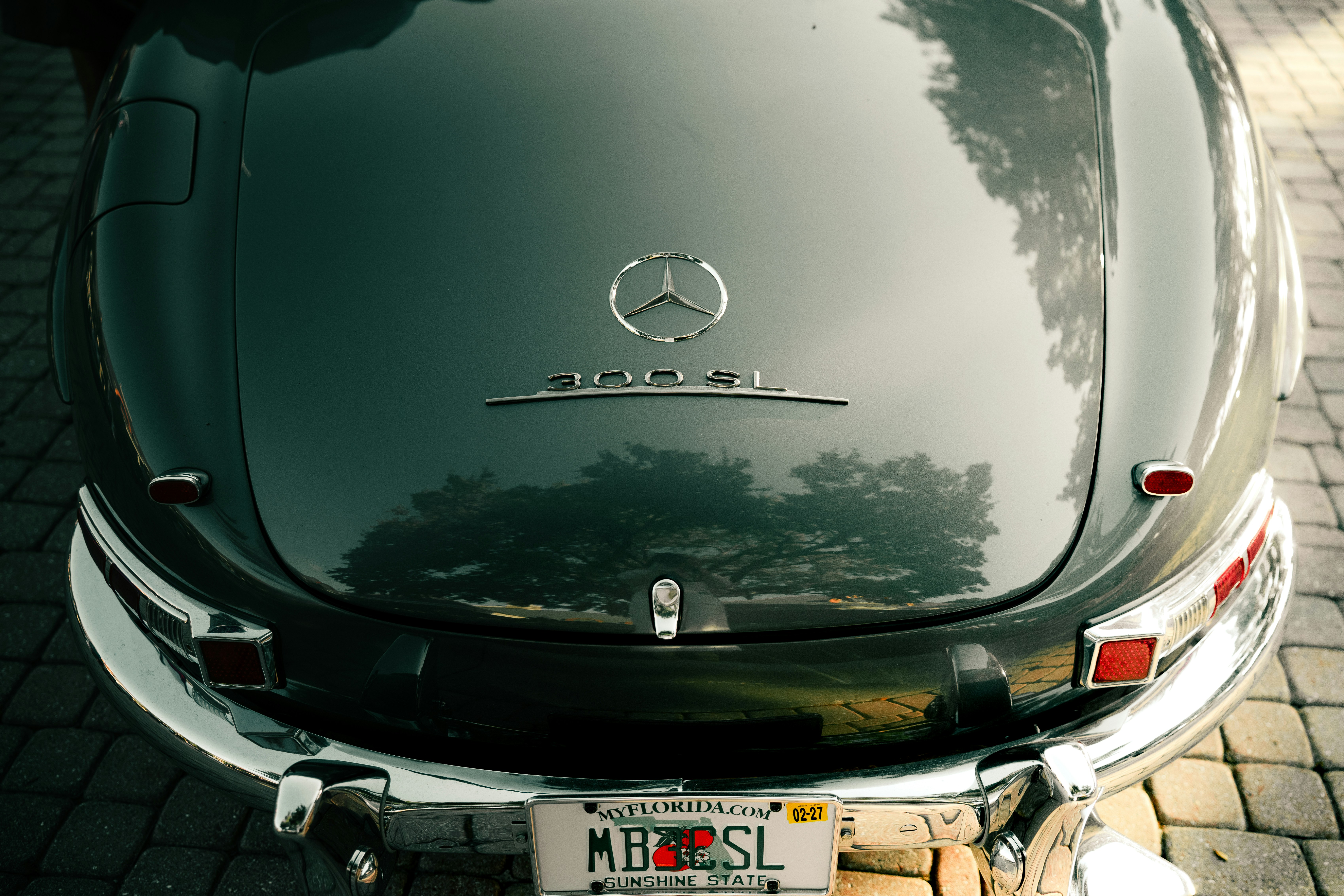 Vintage car with a glossy dark finish reflecting trees and sky on its trunk.