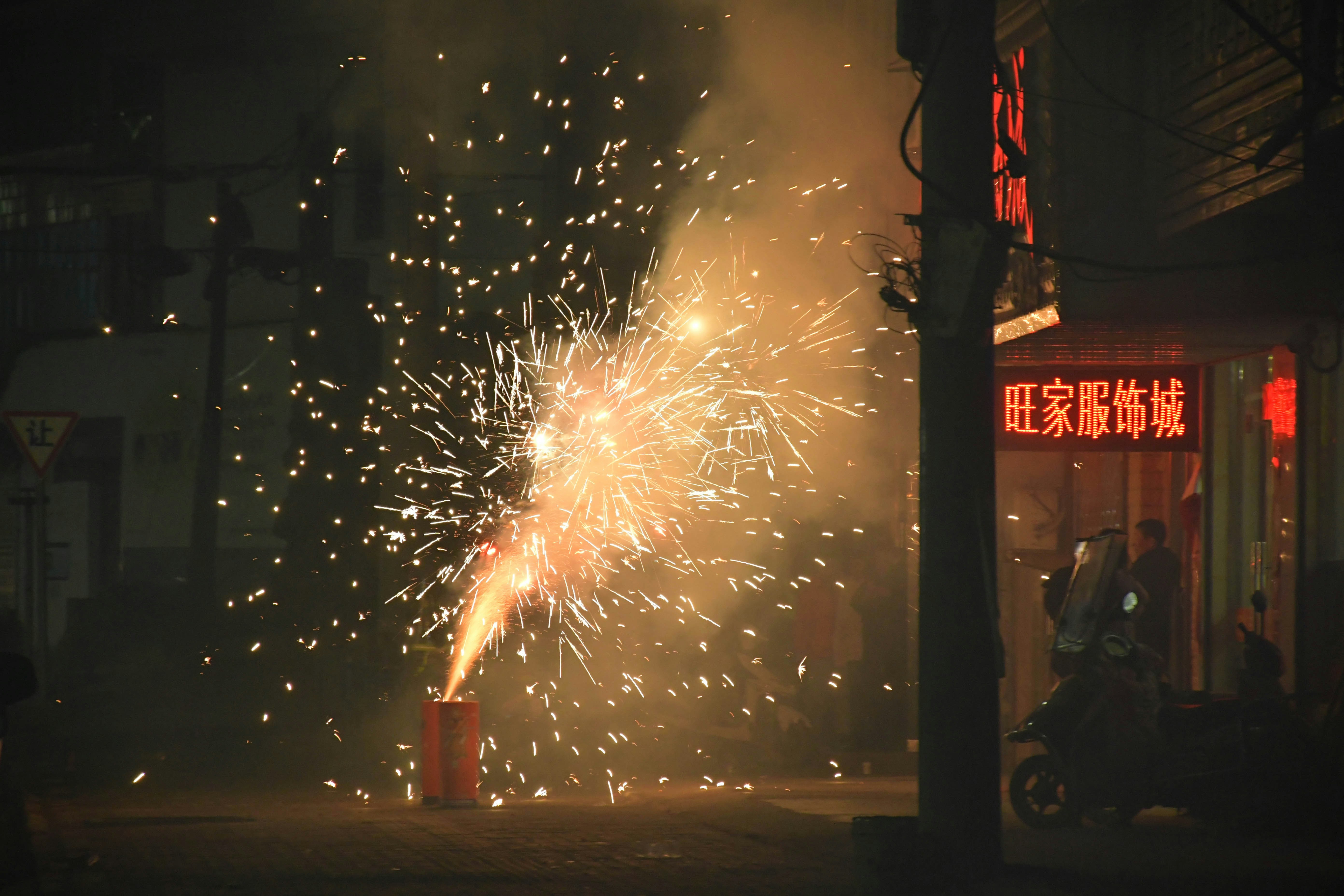 Embers Under Neon: A Night Street Spark Fountain Illuminates the Storefront