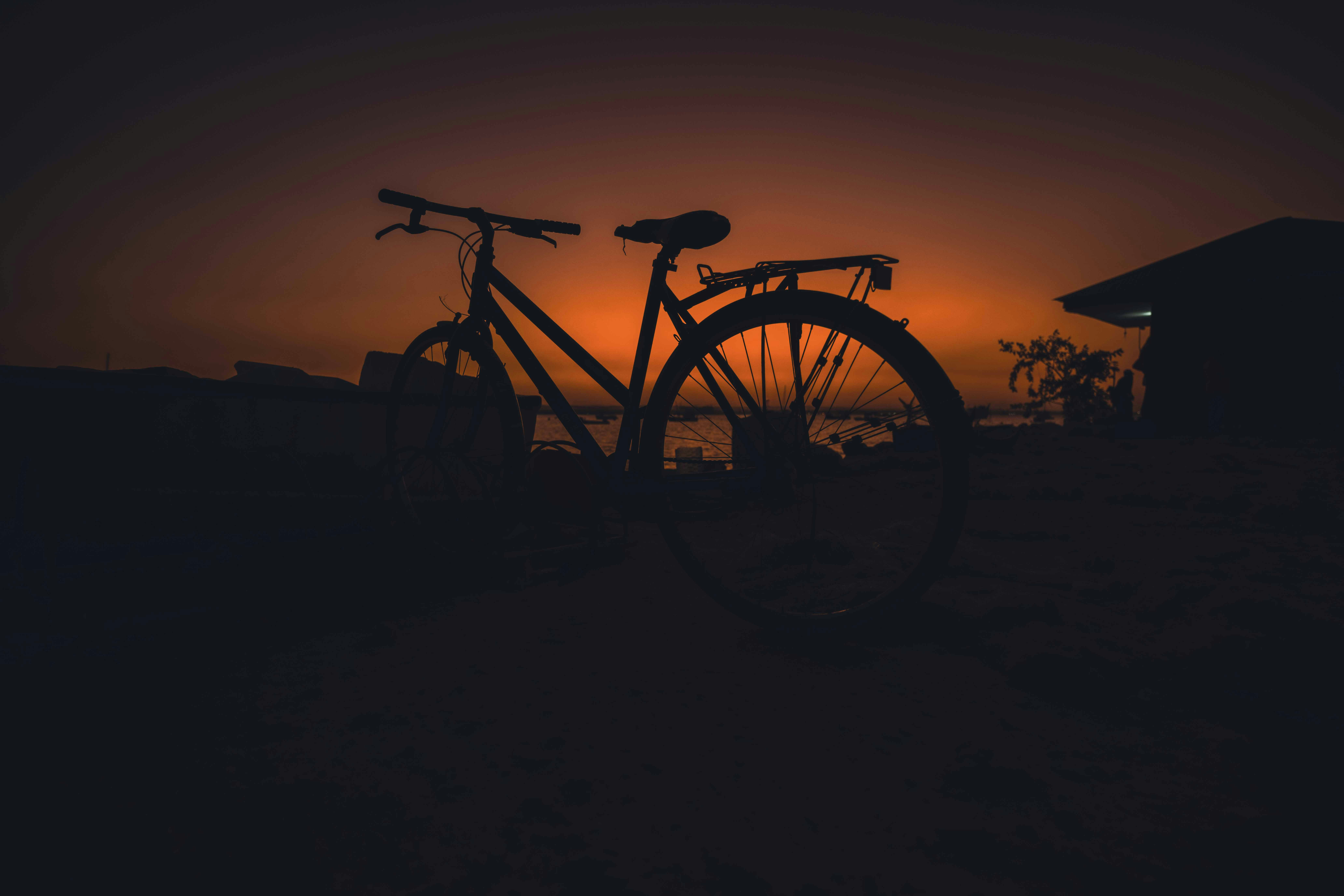 Silhouette of a bicycle against a vibrant orange sunset sky.