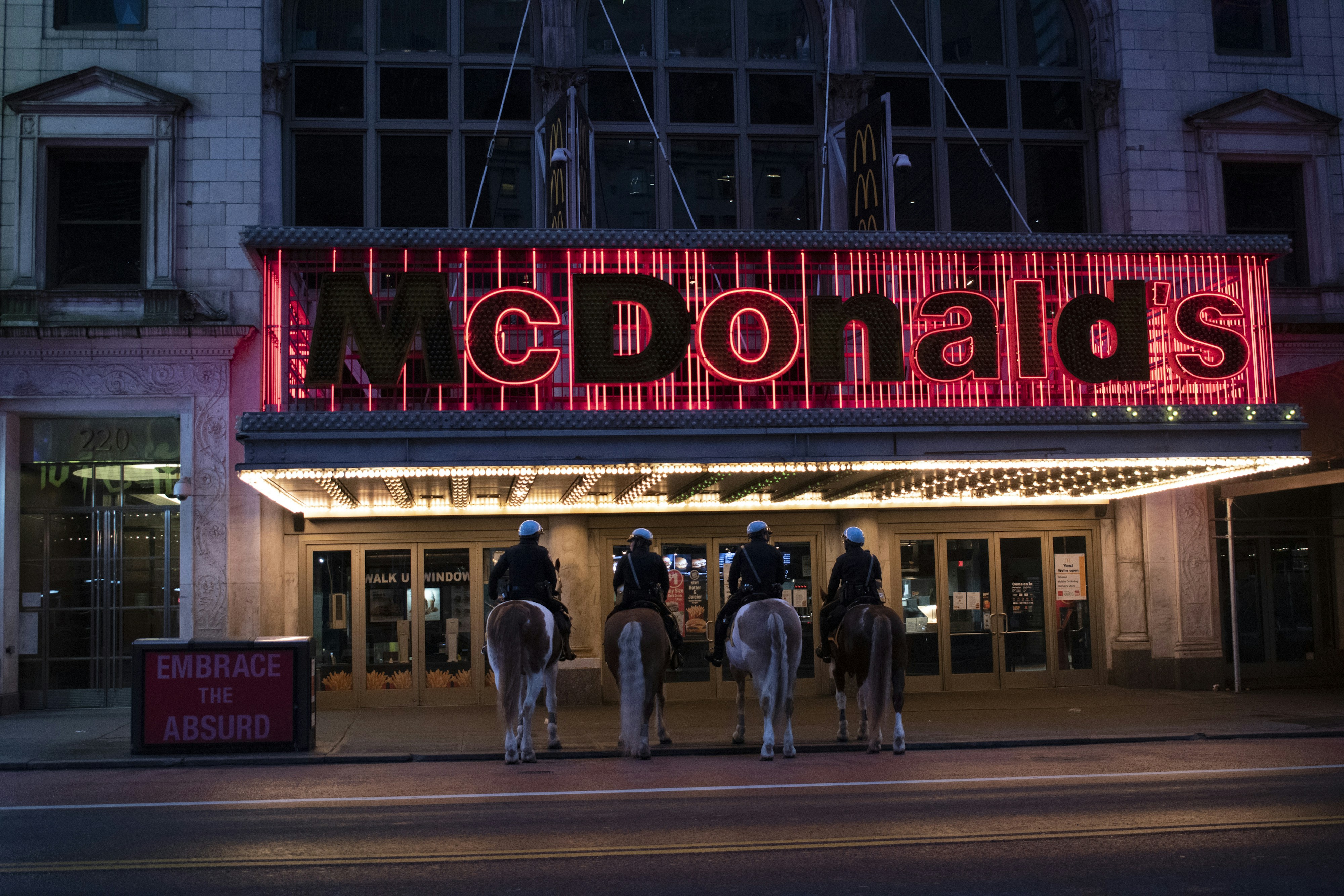 Three mounted police officers beneath a brightly lit McDonald's marquee at night.