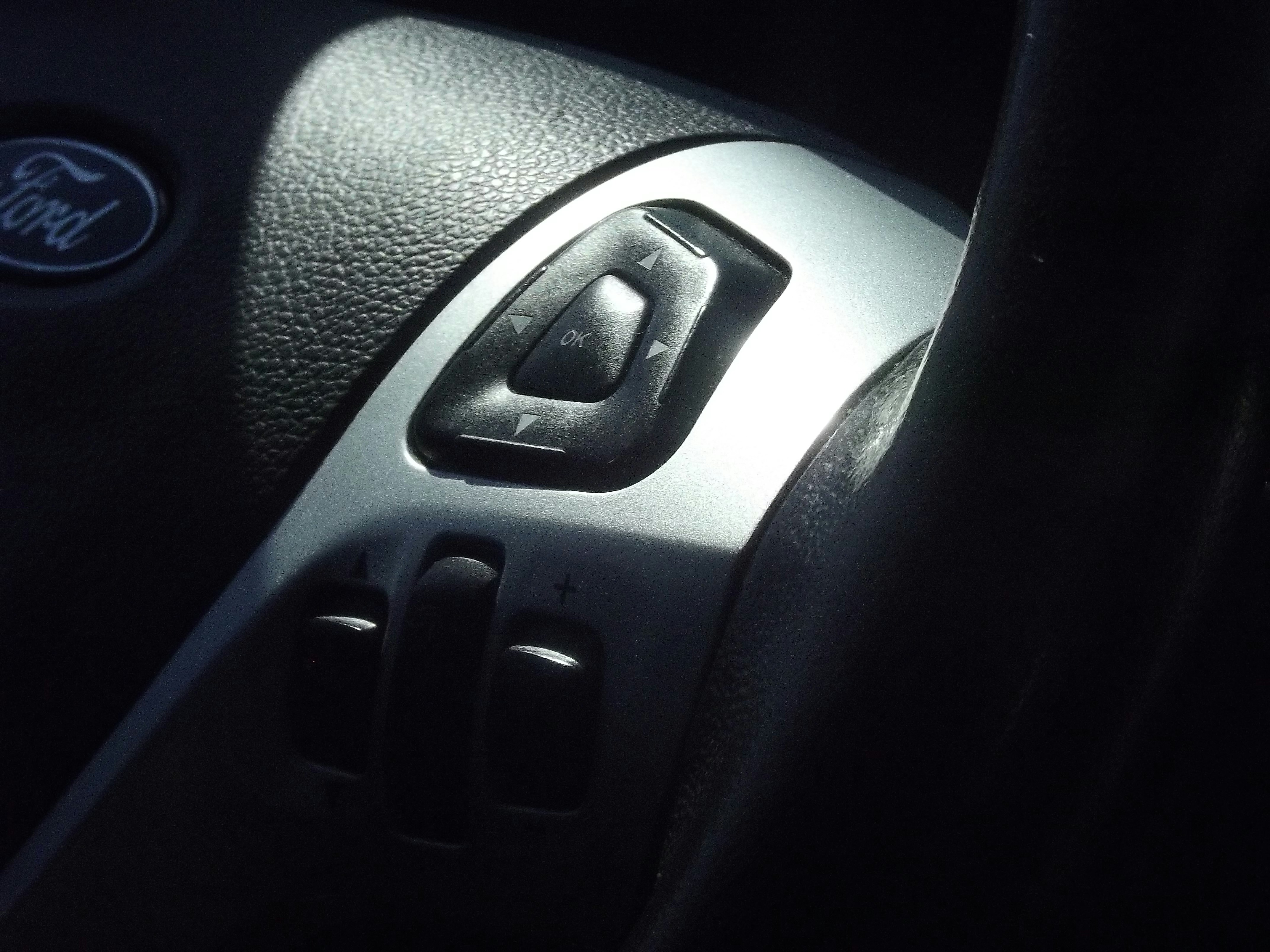 Close-up of a car's control panel featuring buttons for navigation and audio settings. The sleek design highlights modern automotive technology.