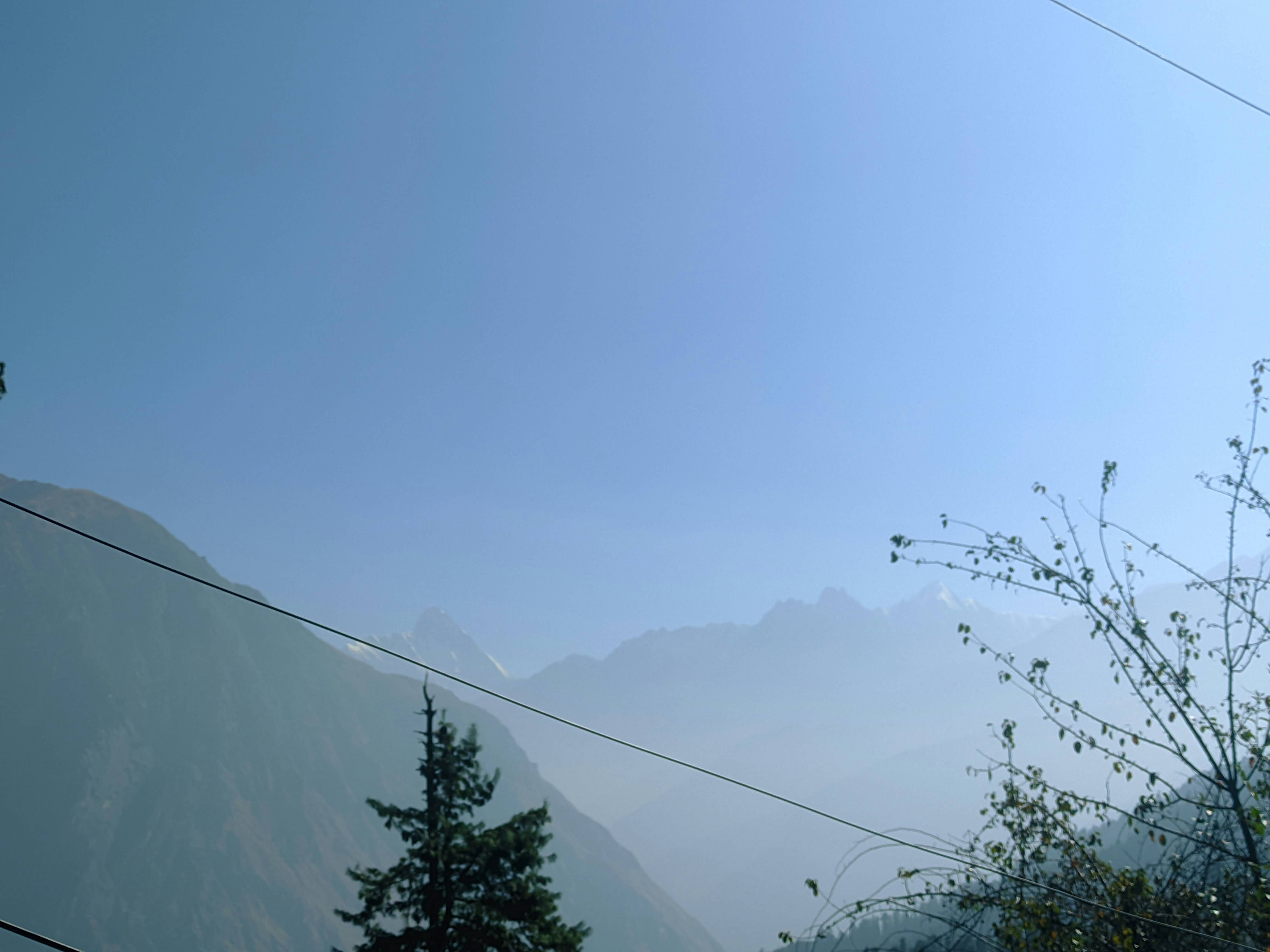 Misty mountain landscape with a clear blue sky and silhouetted trees.