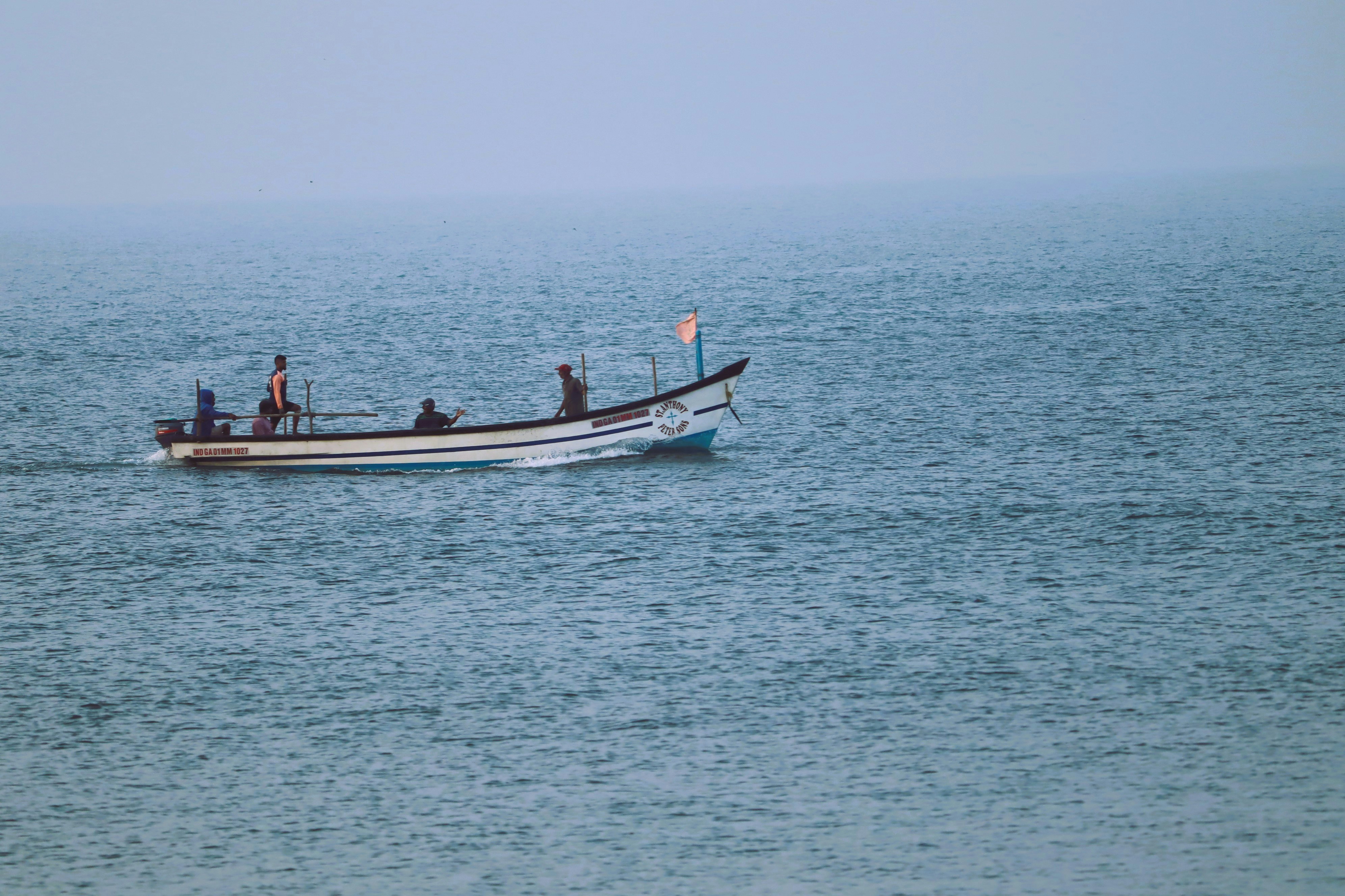 A fishing boat gliding through calm waters, with fishermen engaged in their daily routine. The gentle waves reflect the soft hues of the sky.