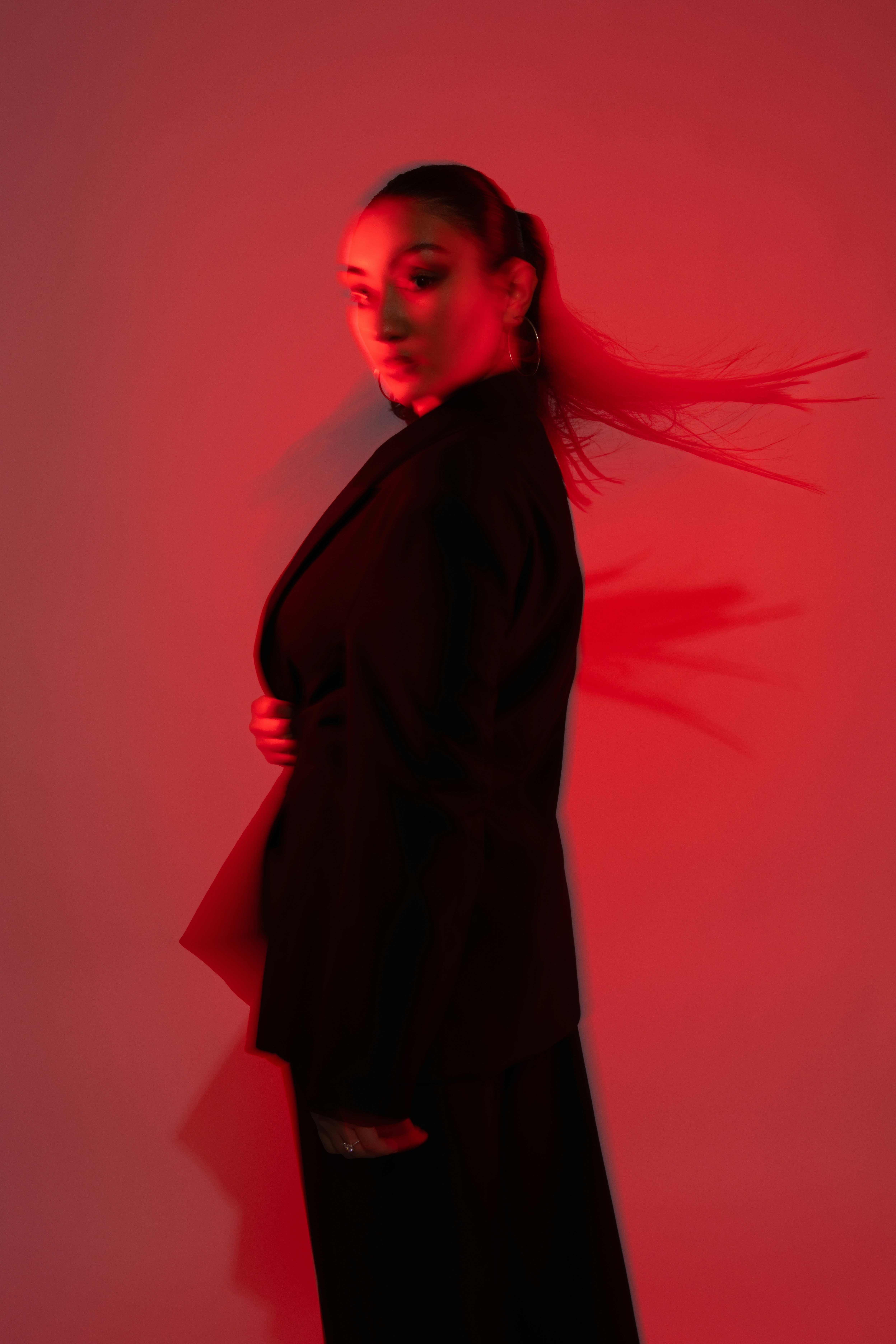 A woman in a sleek black outfit poses with a flowing motion against a vibrant red backdrop, capturing a sense of movement and style.