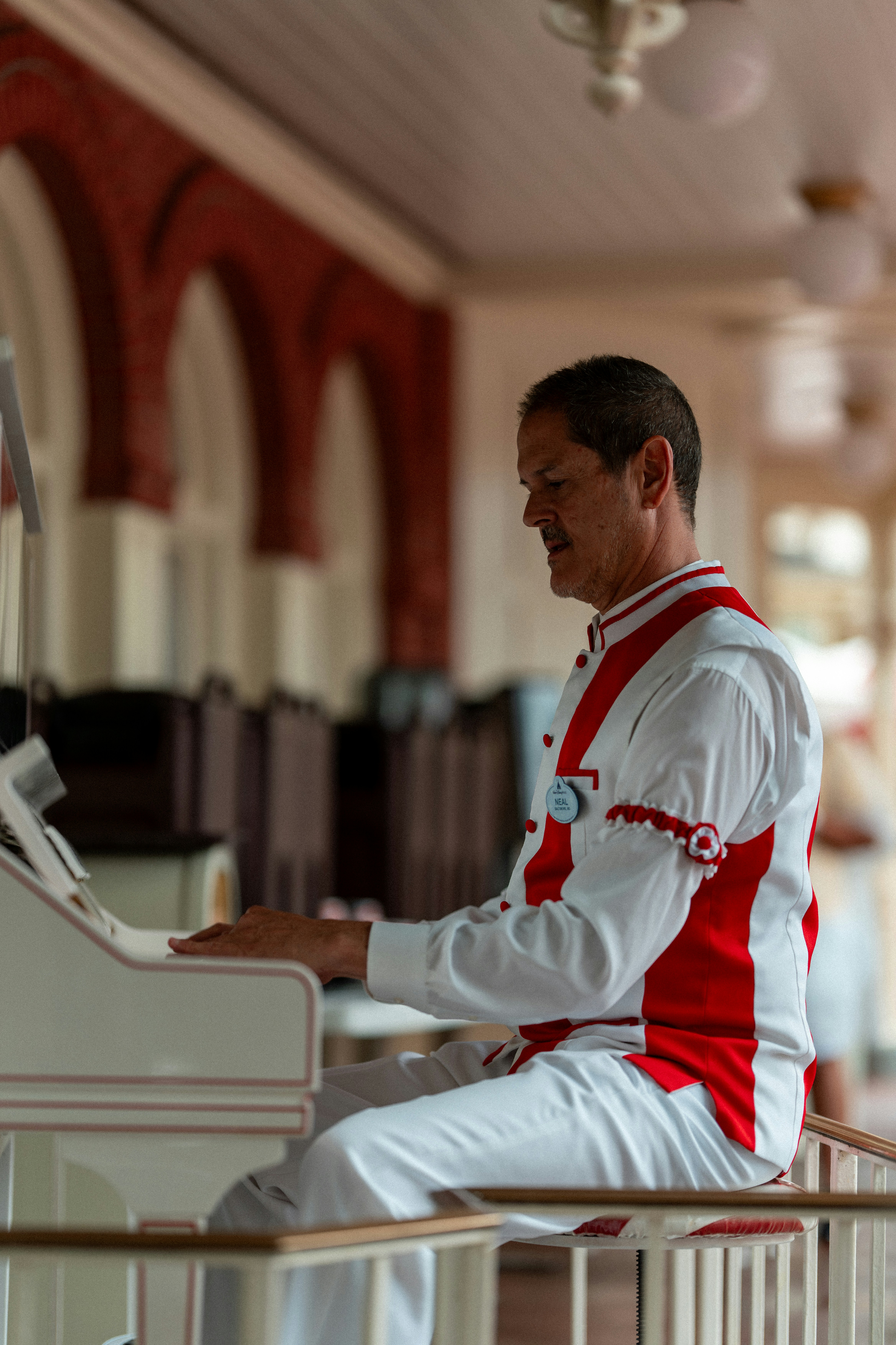 Musician in a red and white uniform playing a piano at an outdoor venue with arched brick architecture.
