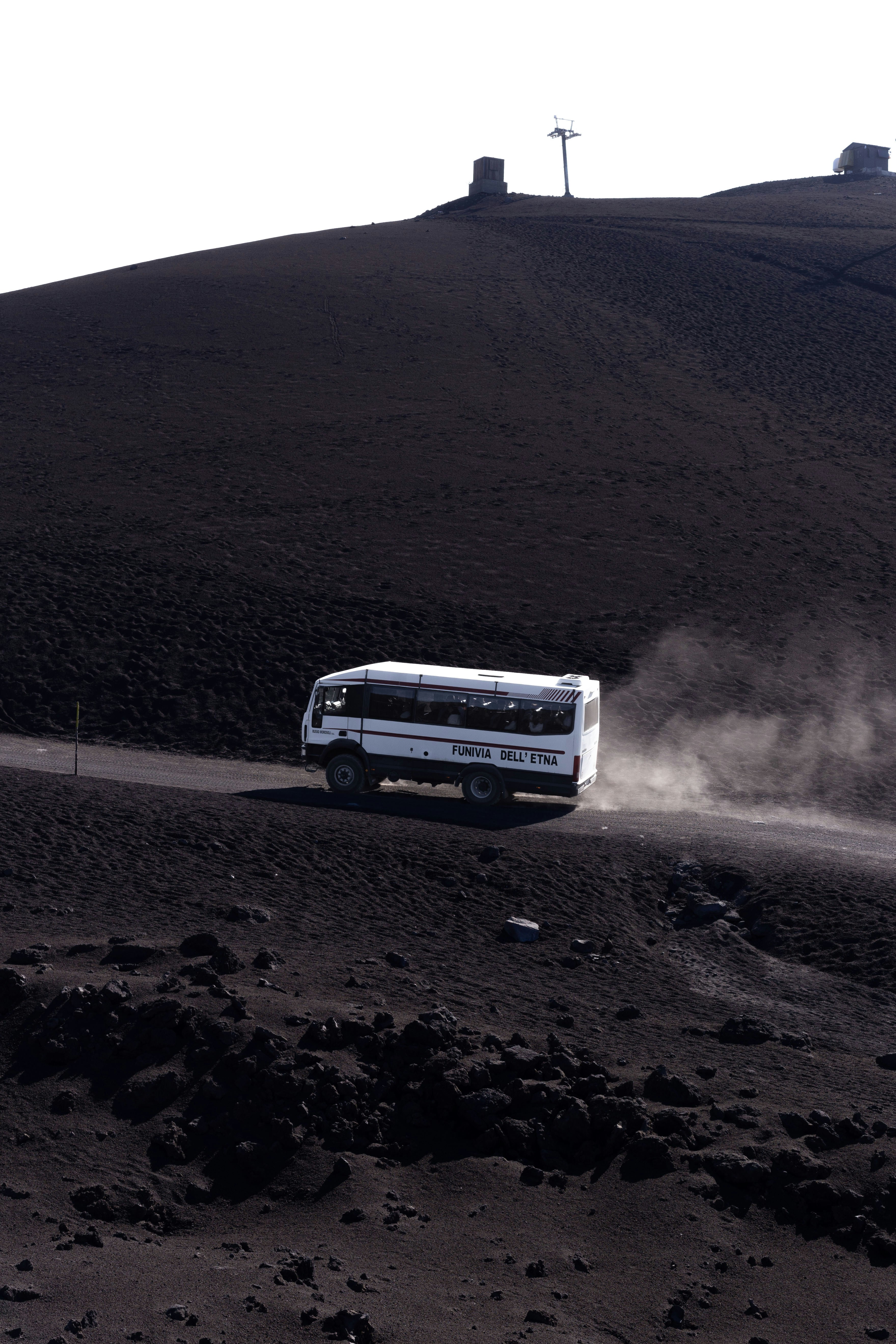 Dust Trail on a Lunar Lava Field: White Bus Climbing the Slope