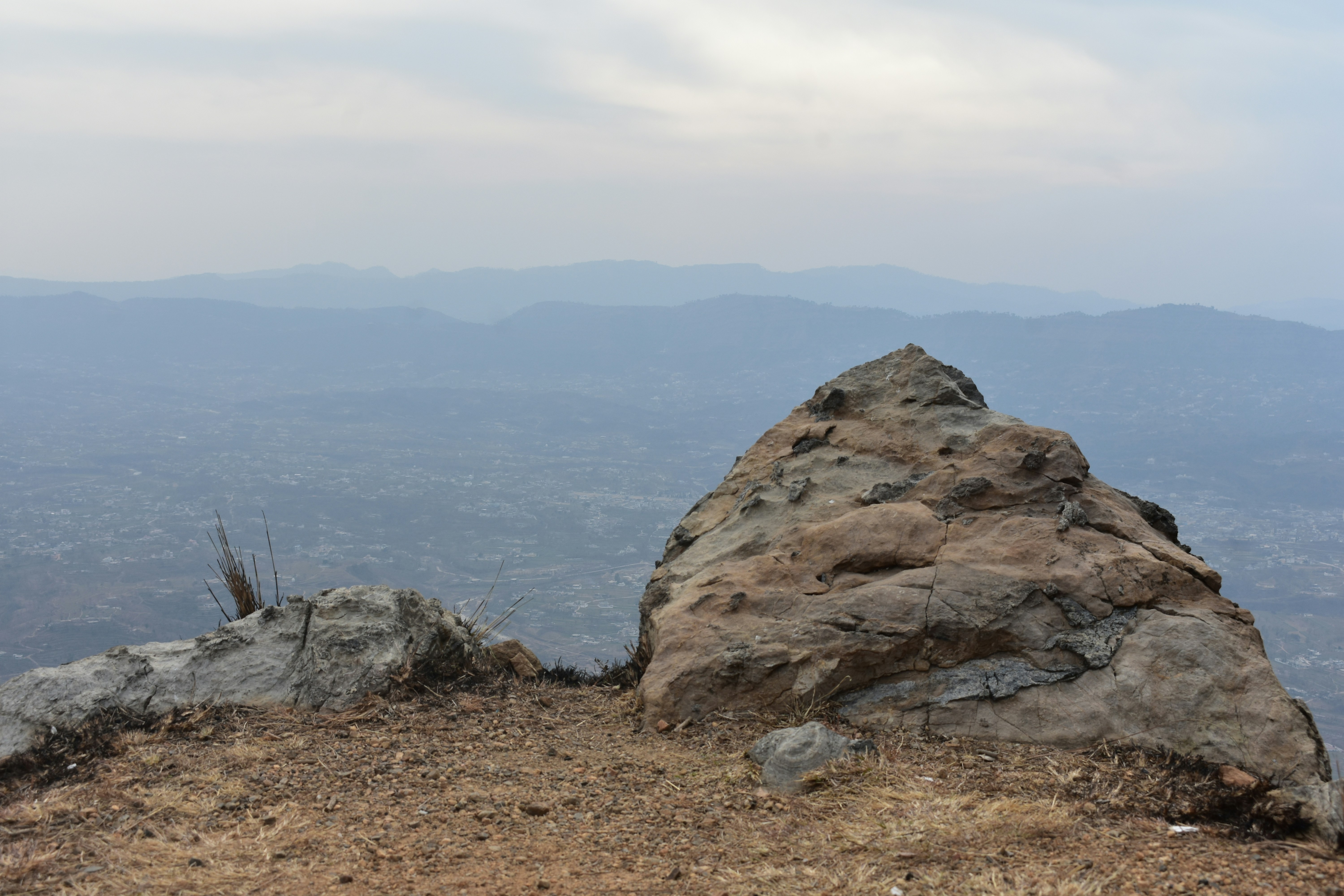 Rocky outcrop overlooking hazy mountain ranges under a cloudy sky.