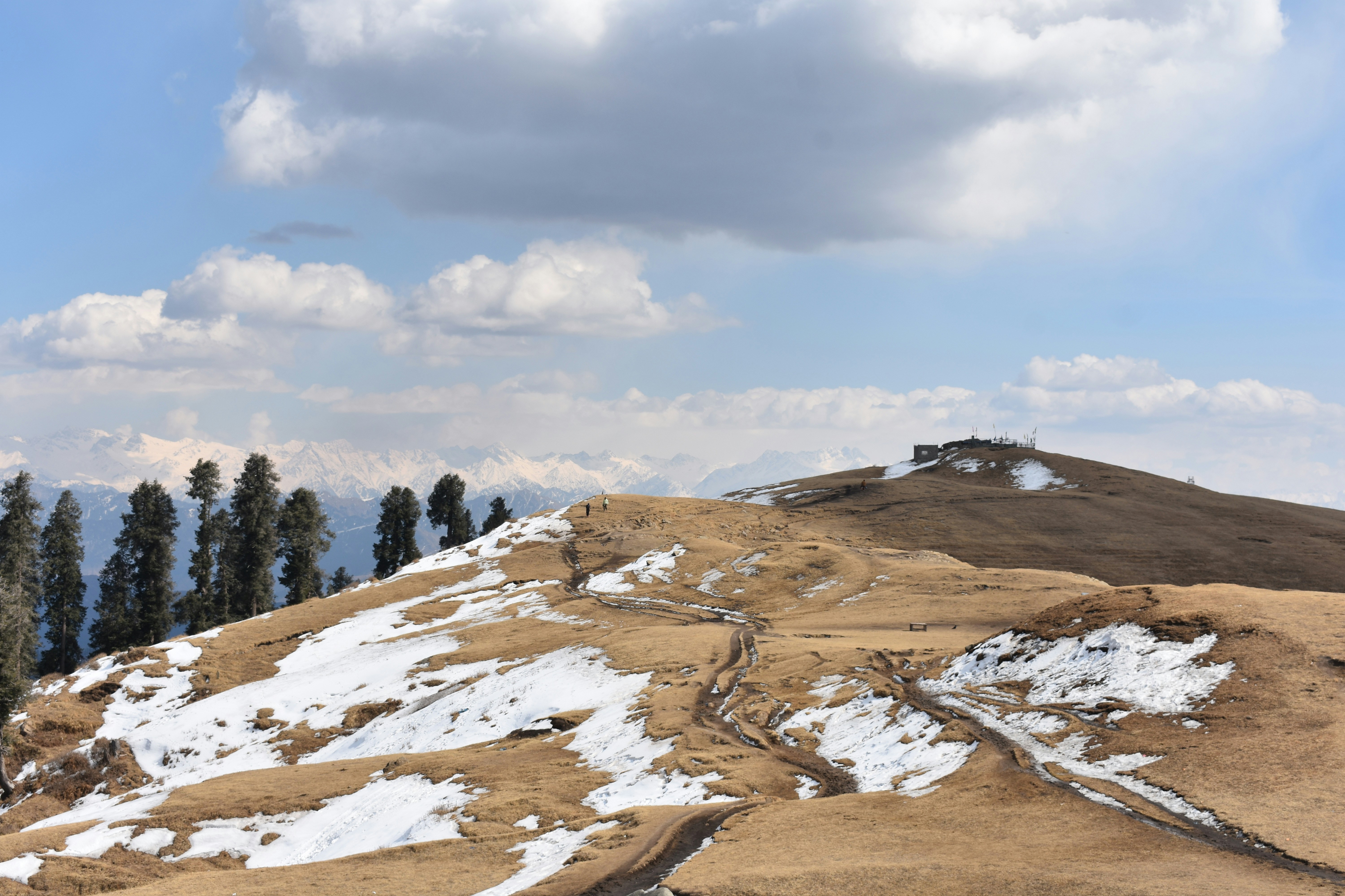 Switchbacks across a snow-dusted ridge toward a lone hilltop beacon