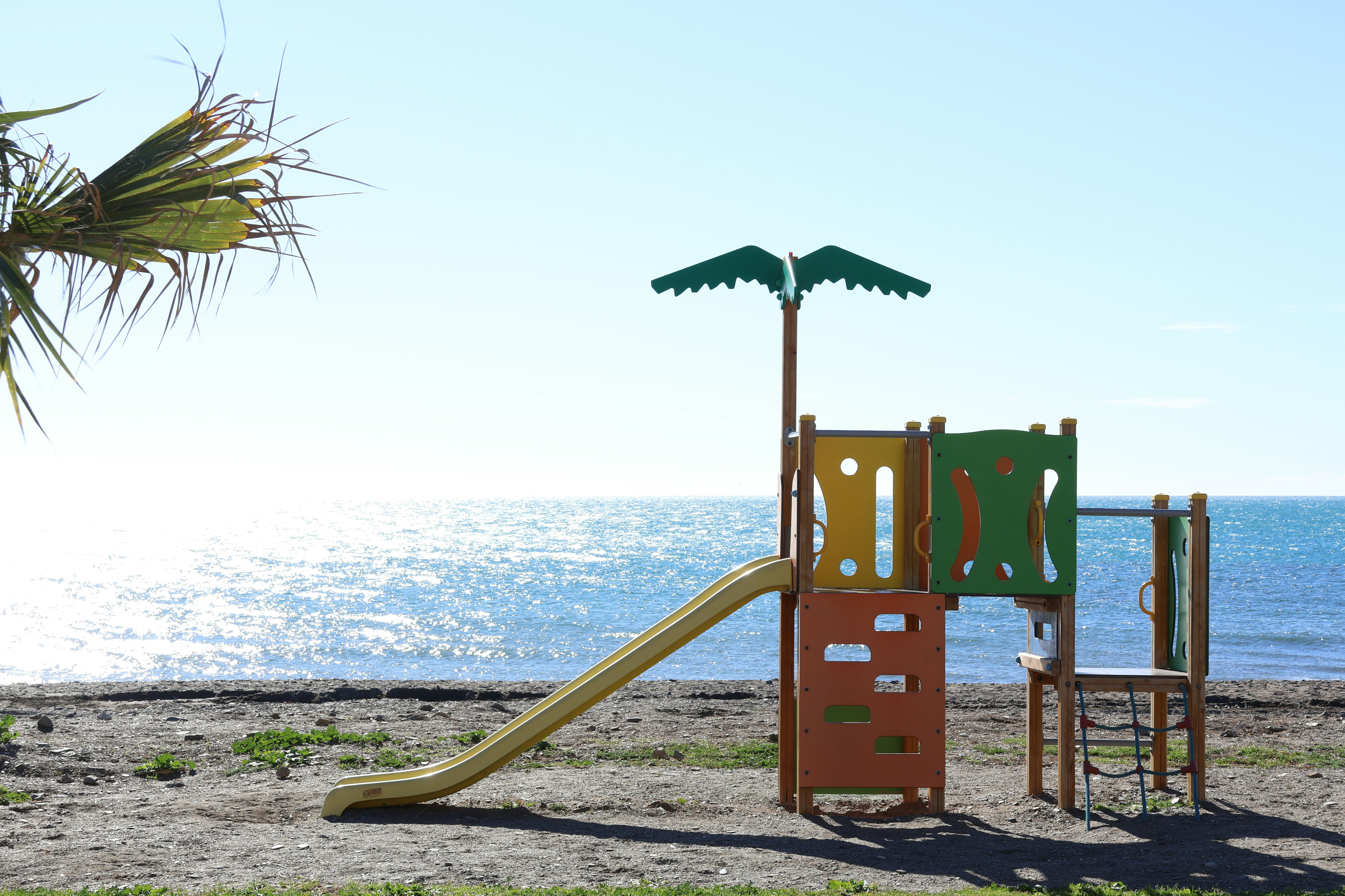 Colorful playground set by the ocean under a clear blue sky.