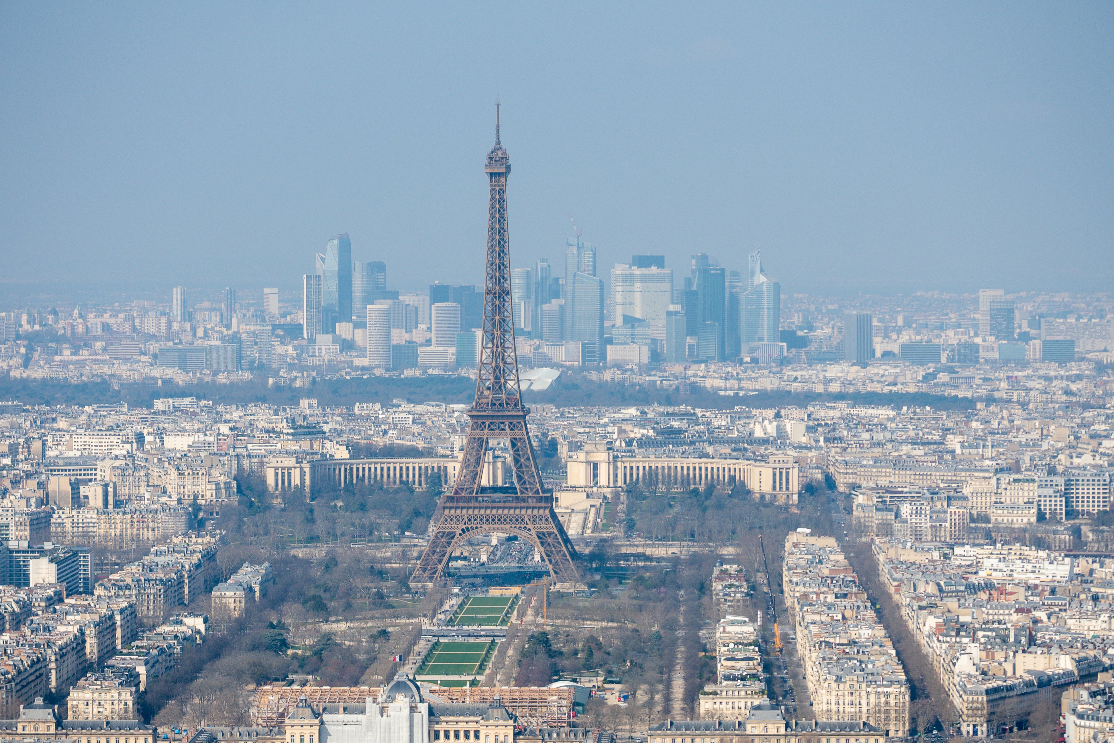Eiffel Tower rises prominently with La Défense skyline in the hazy background.