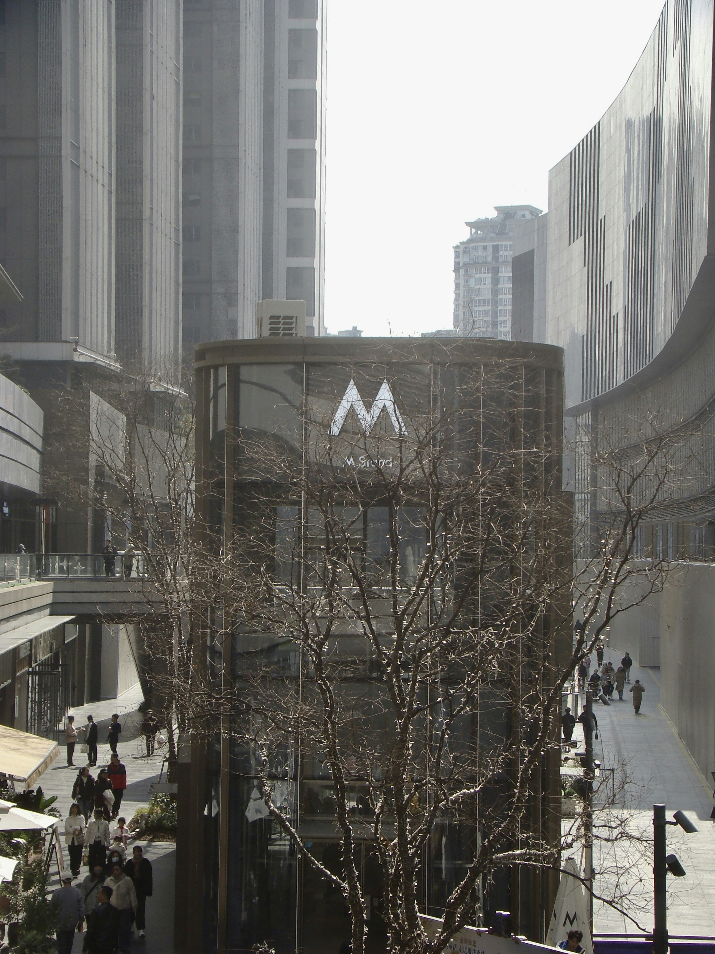 M-Logo Glass Cylinder Anchors a Quiet City Plaza