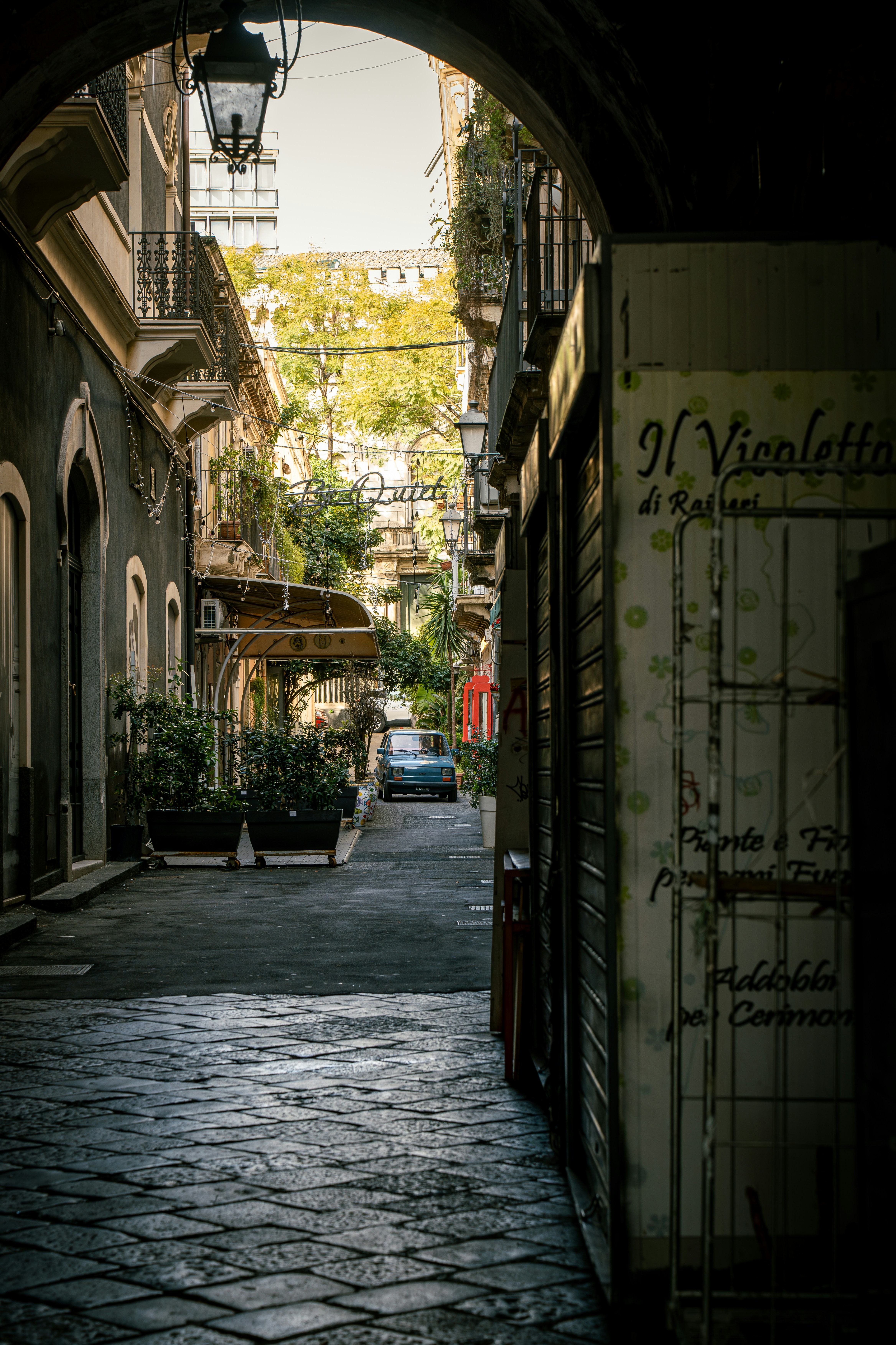 The Archway Convergence: A Quiet Blue Car at the End of a Sunlit Cobblestone Alley