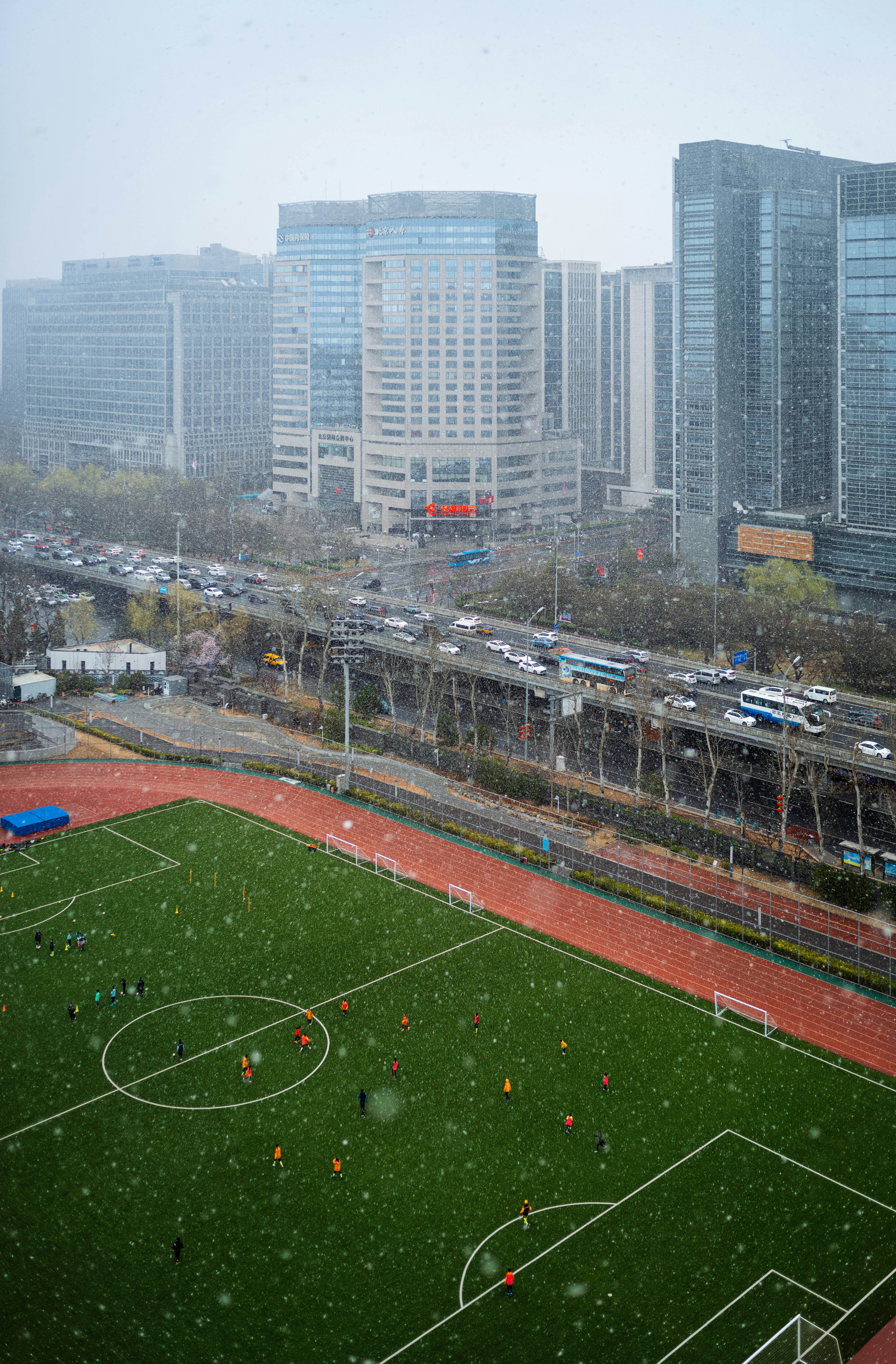 Snow falls over a city with a soccer field. photo – Free Car Image on ...