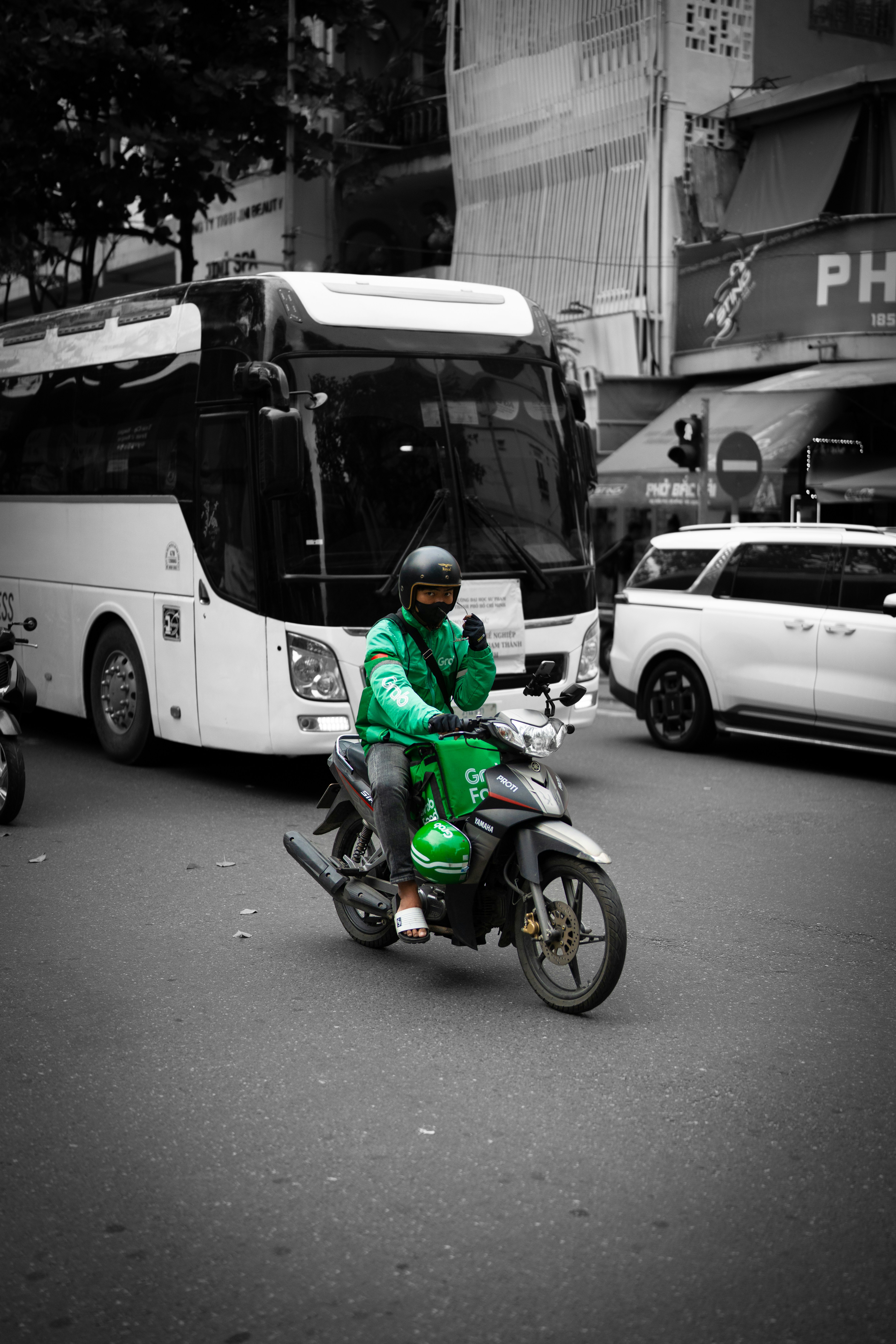 Delivery rider in vibrant green gear navigating a busy city street, surrounded by monochrome vehicles.