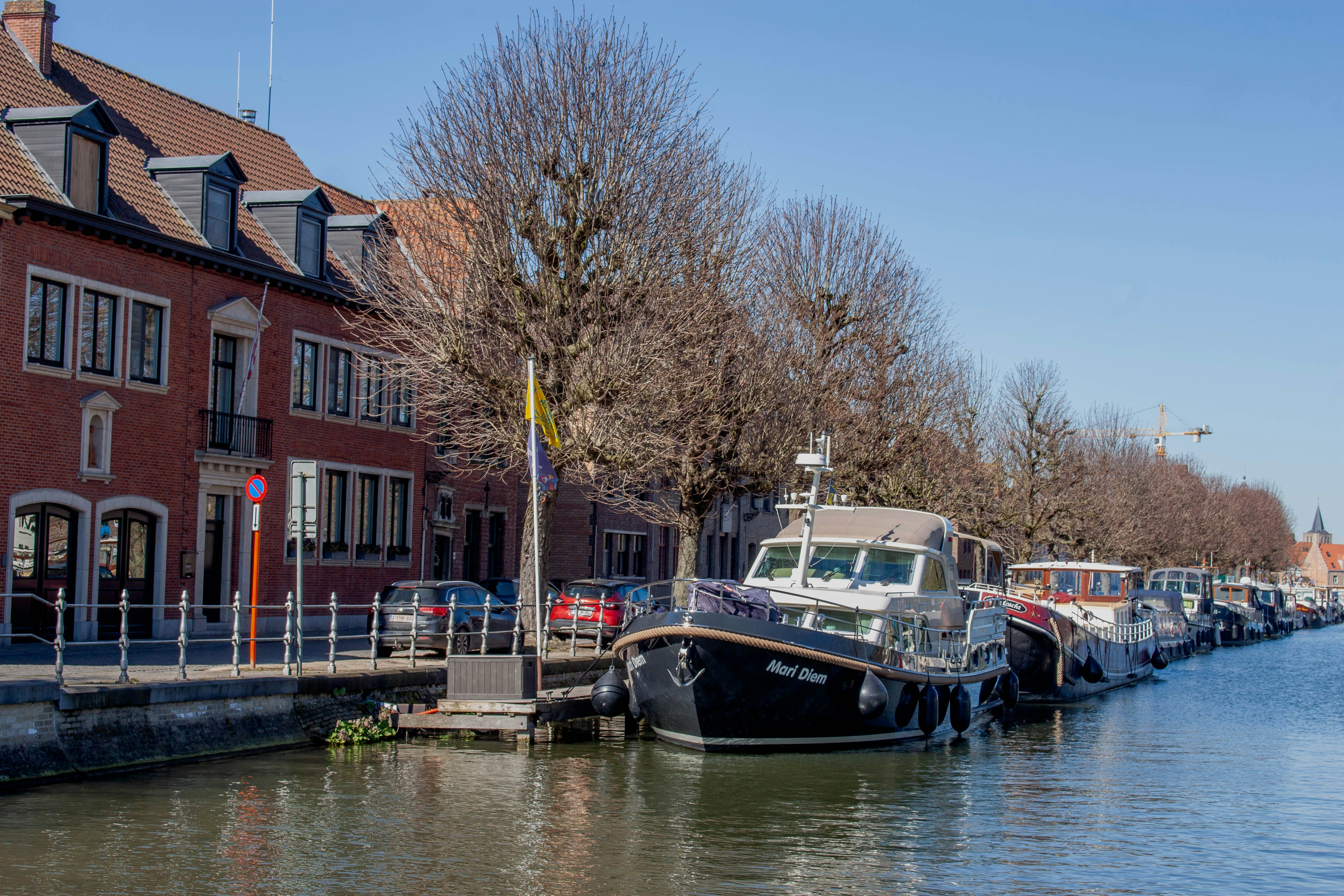 Boats lined along a tranquil canal with brick buildings under a clear blue sky.