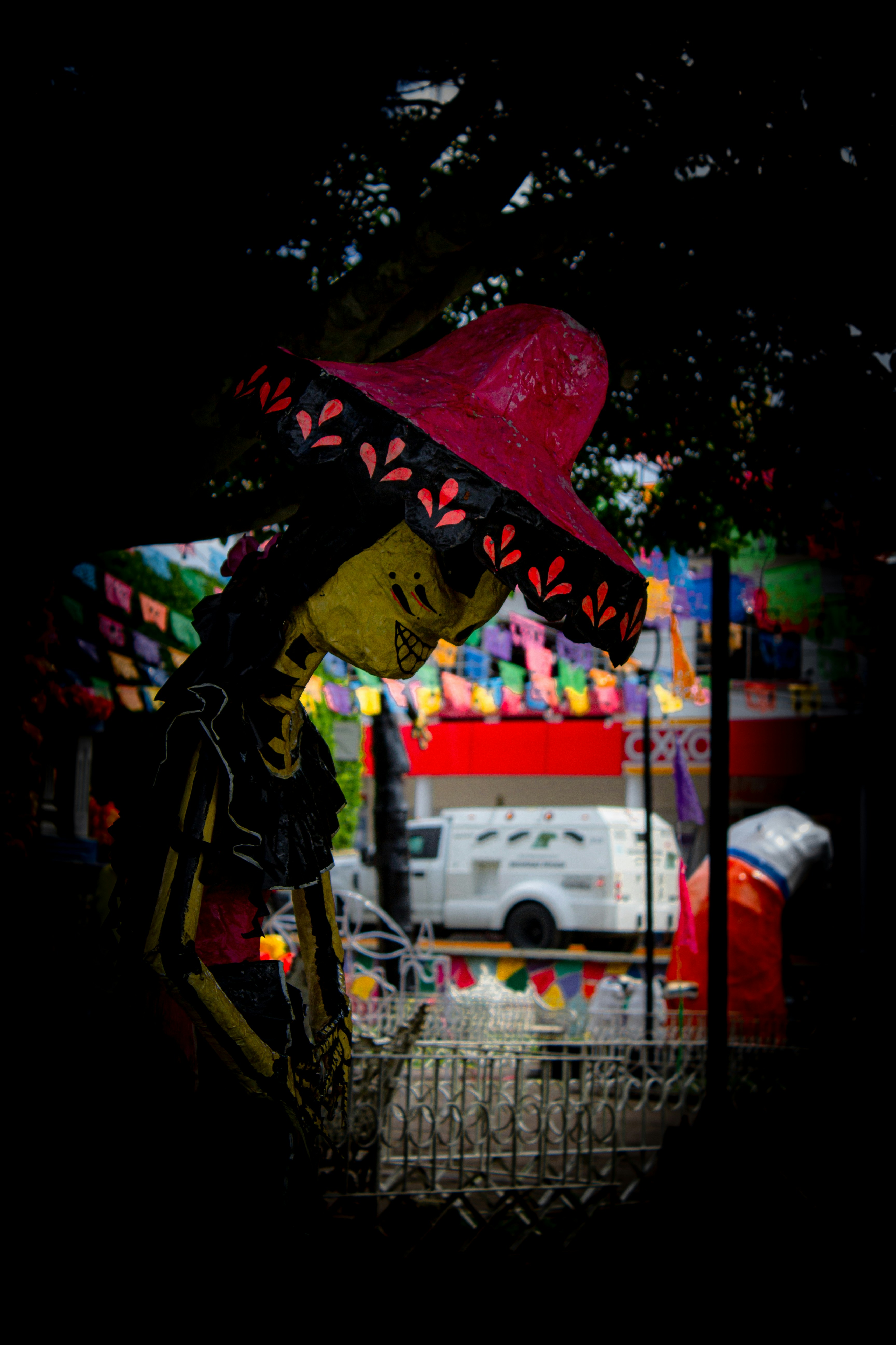 Colorful paper mache figure in a sombrero stands among festive banners and vibrant urban backdrop.