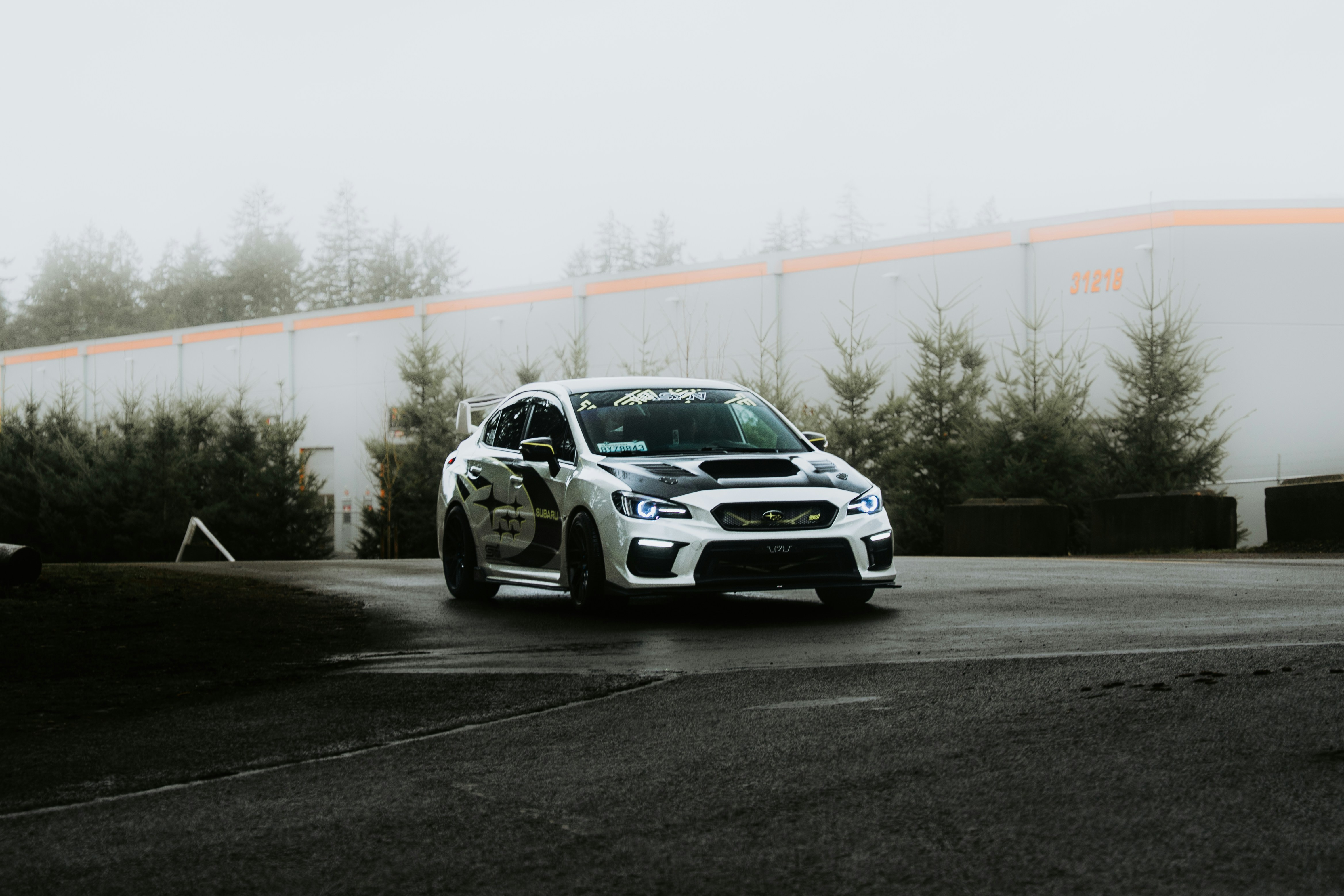 A white subaru drives past a building on a foggy day. photo – Free ...