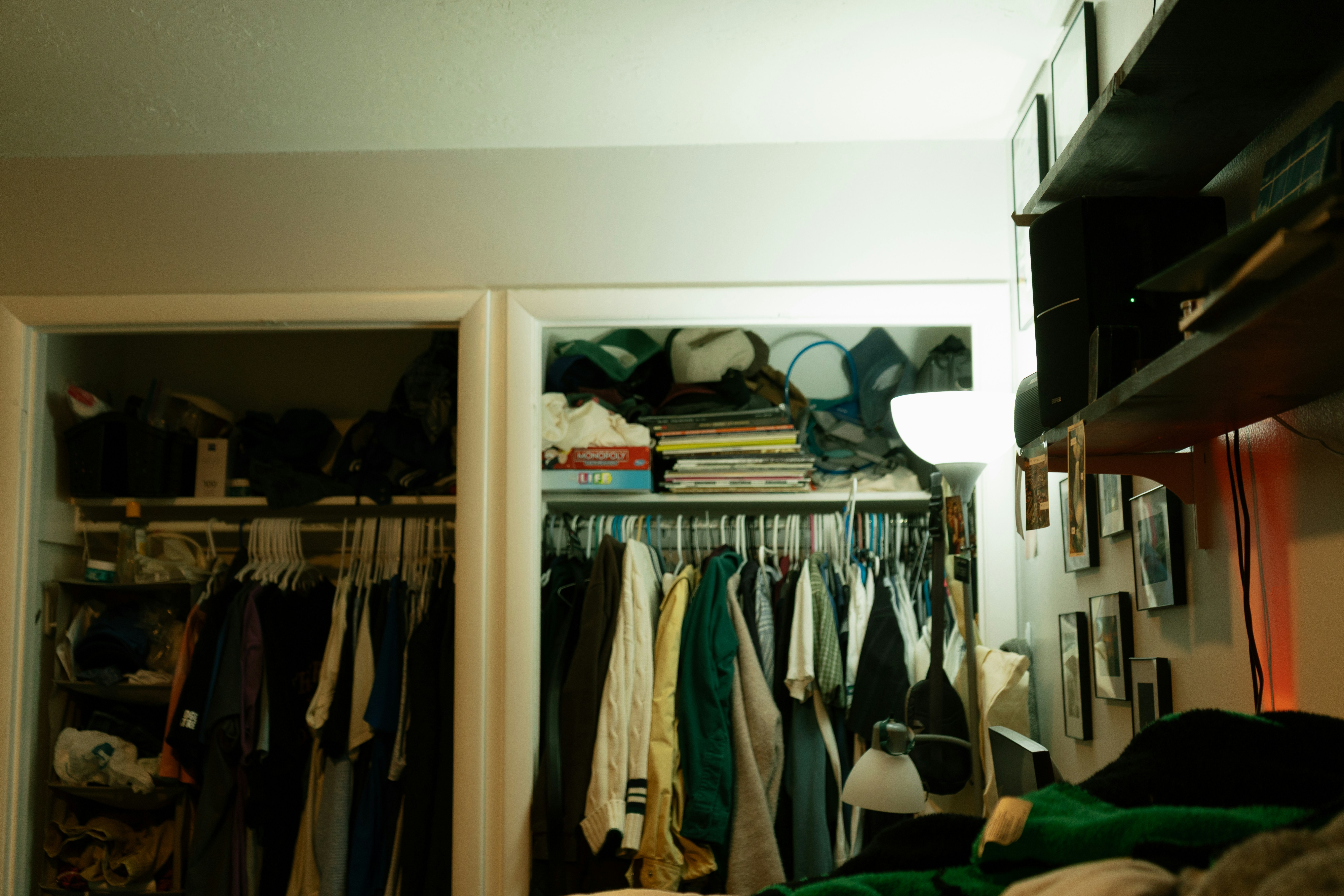 A cluttered closet filled with hanging clothes and stacked items, illuminated by a soft lamp. The scene captures the essence of a lived-in space.