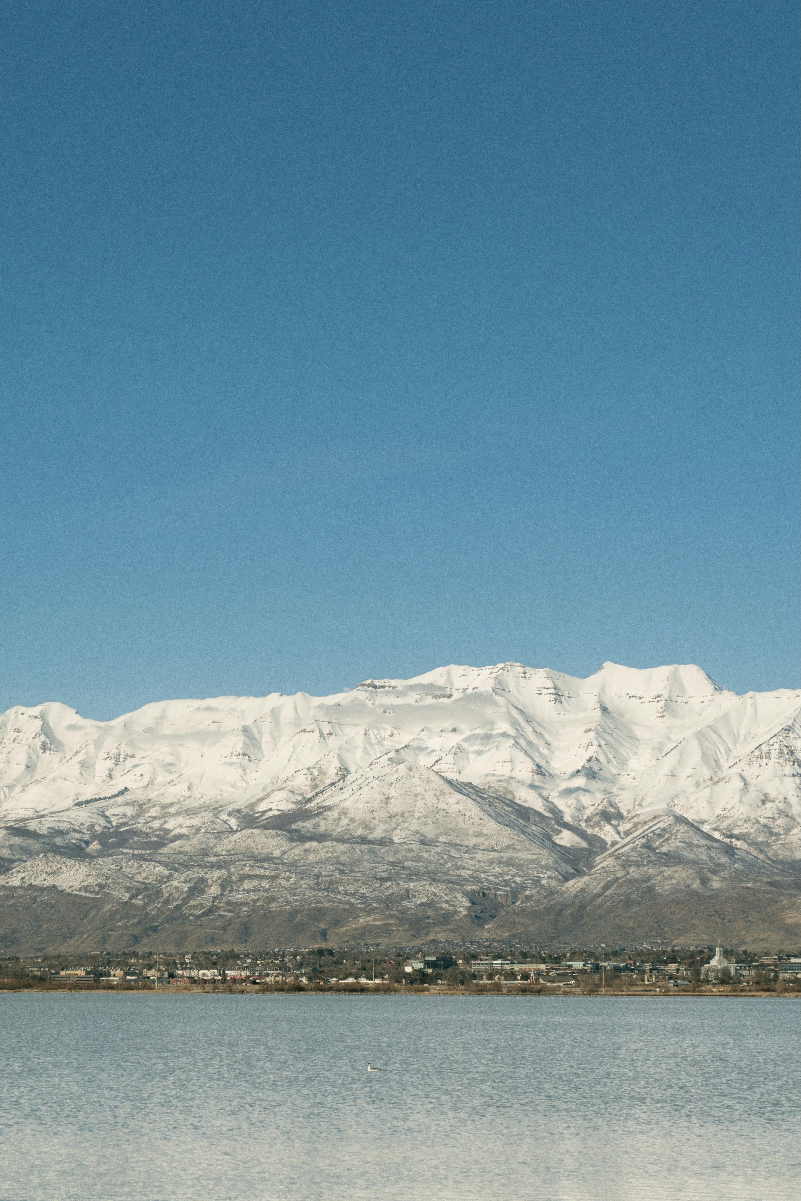 Snow-capped mountains reflect in a tranquil lake under a clear blue sky.
