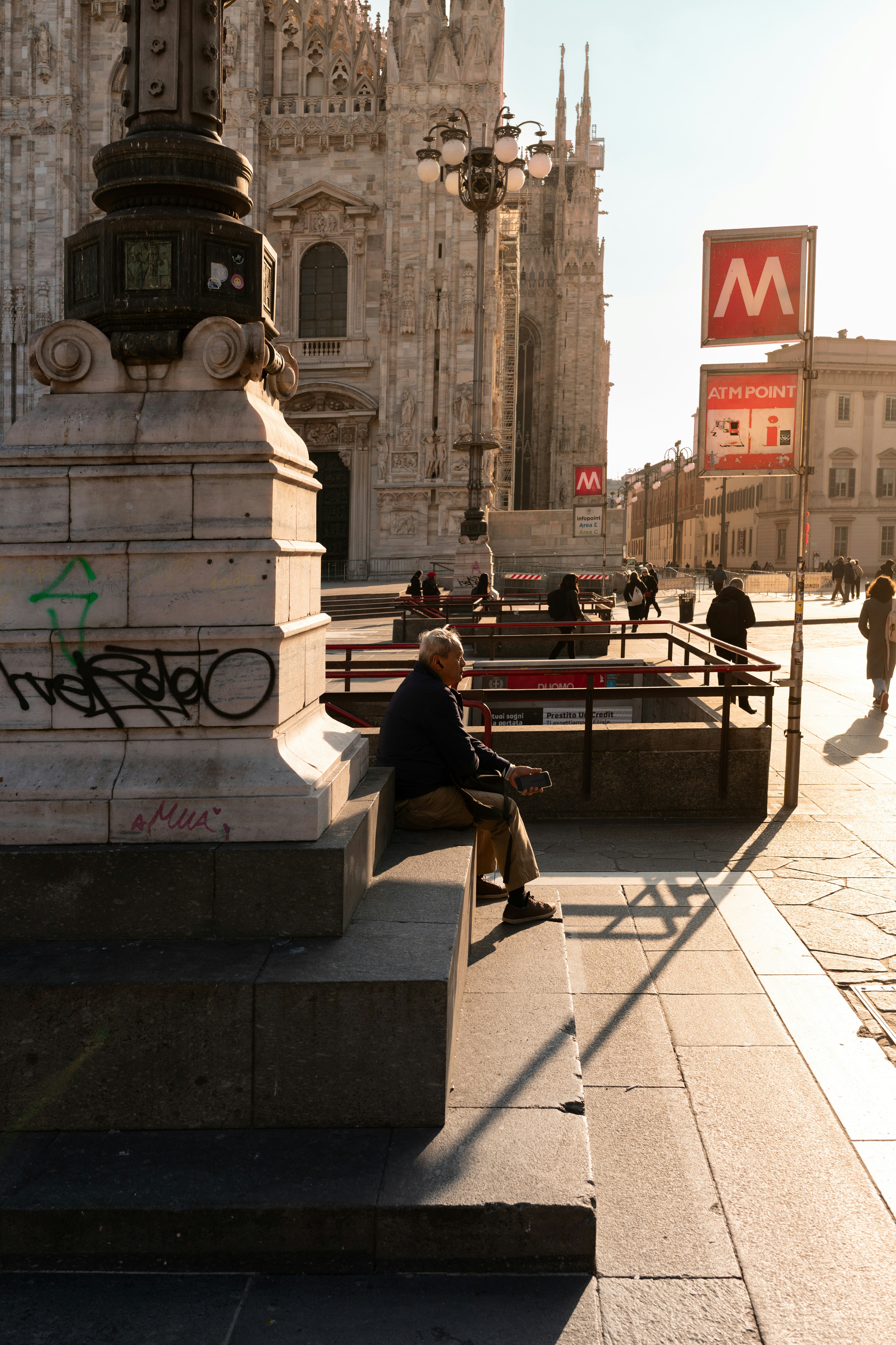 People sitting and walking near a historic cathedral with warm sunlight casting long shadows.