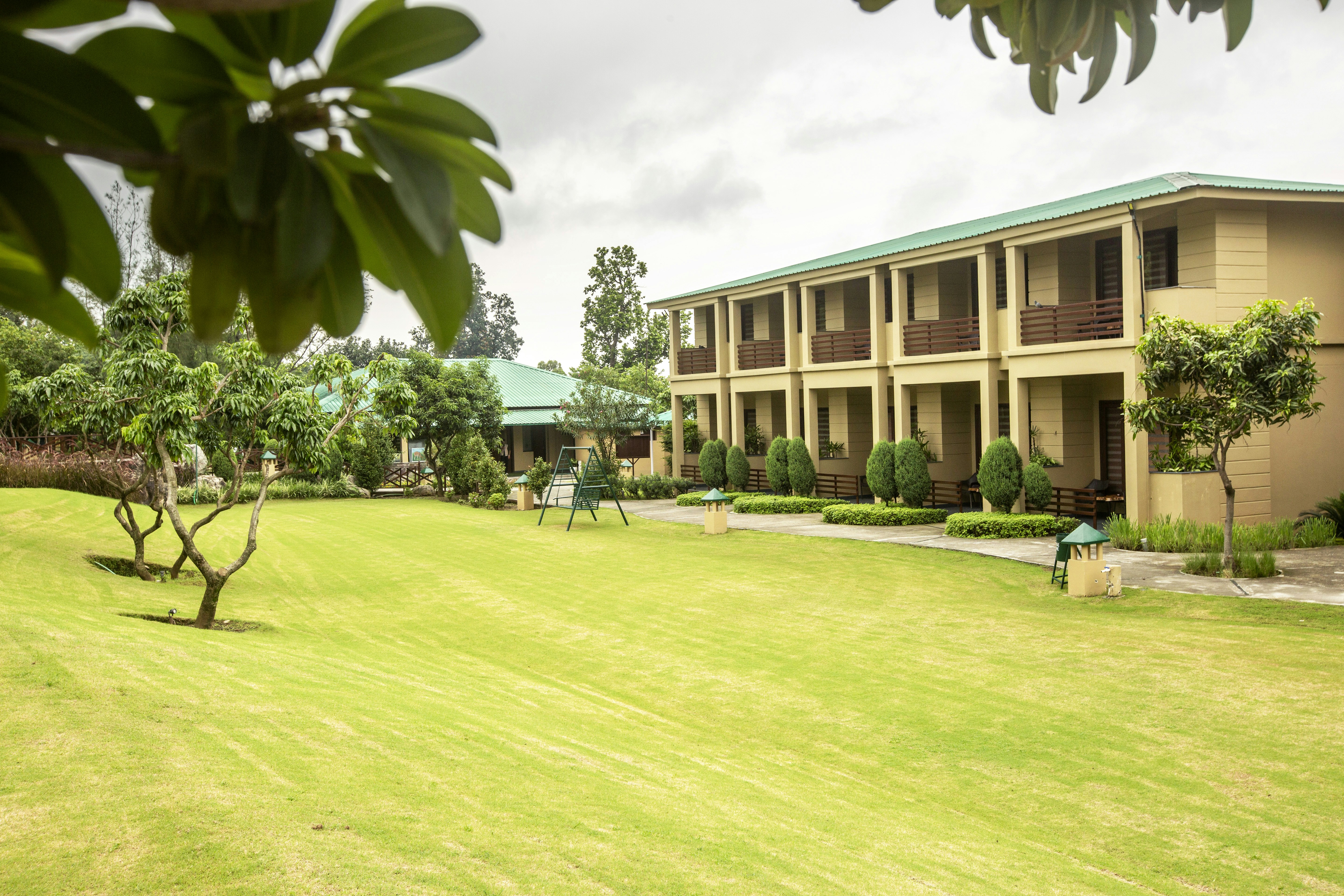 Lush green lawn with a modern two-story resort building under a cloudy sky.