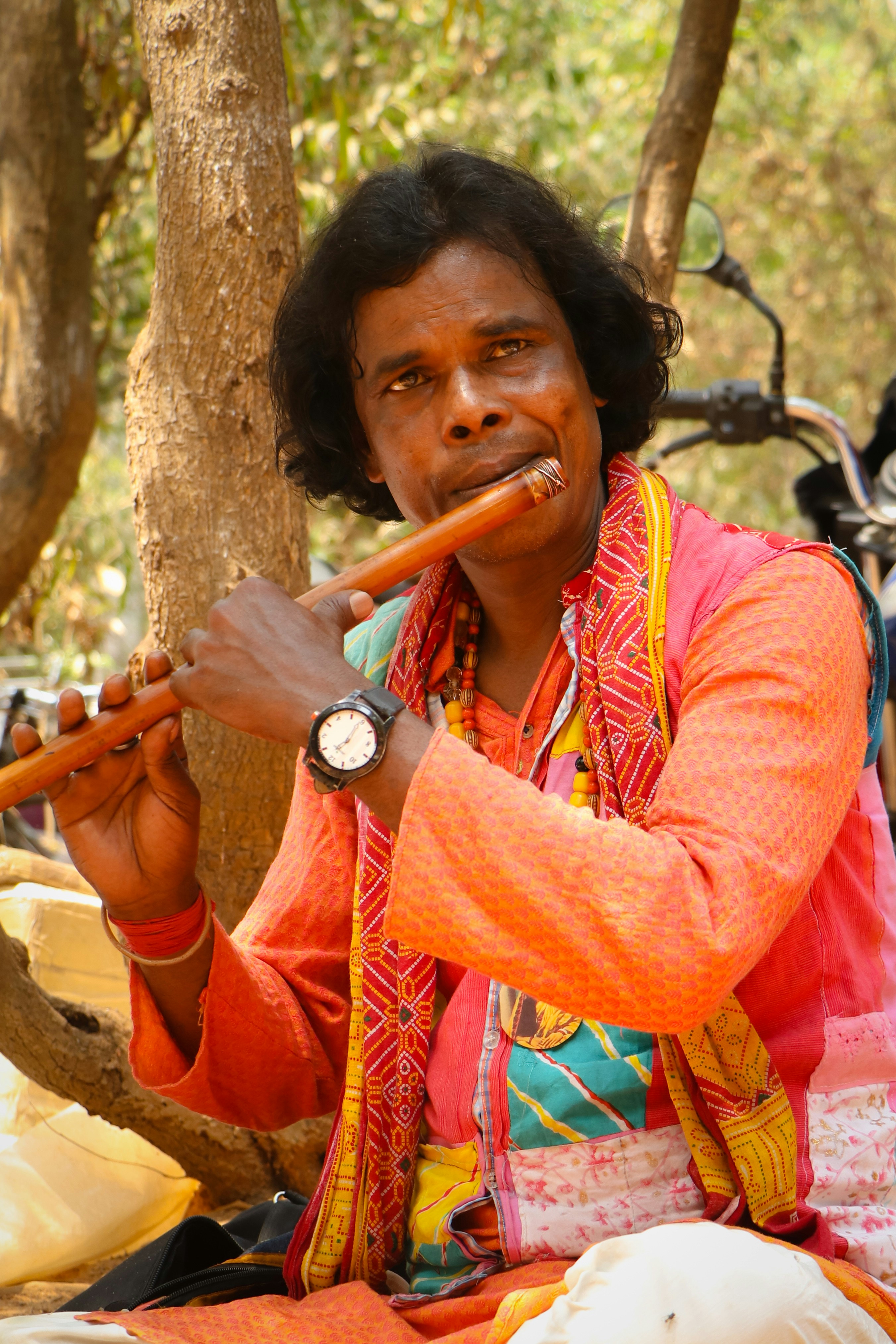 A musician passionately playing a bamboo flute amidst a wooded backdrop, dressed in vibrant traditional attire.