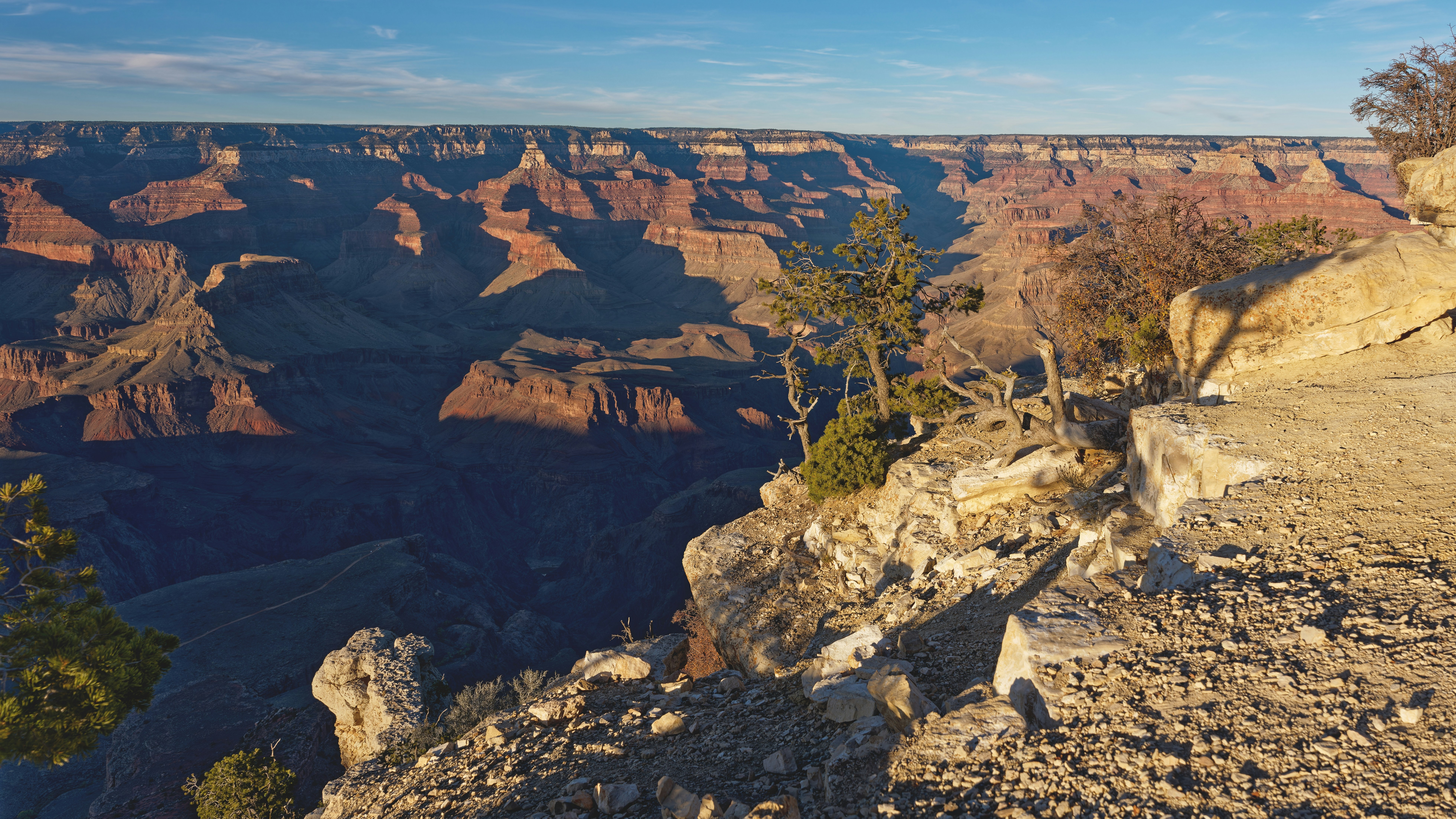 Rugged cliffs of the Grand Canyon illuminated by warm sunlight, with shadows accentuating the terrain's depth and texture.