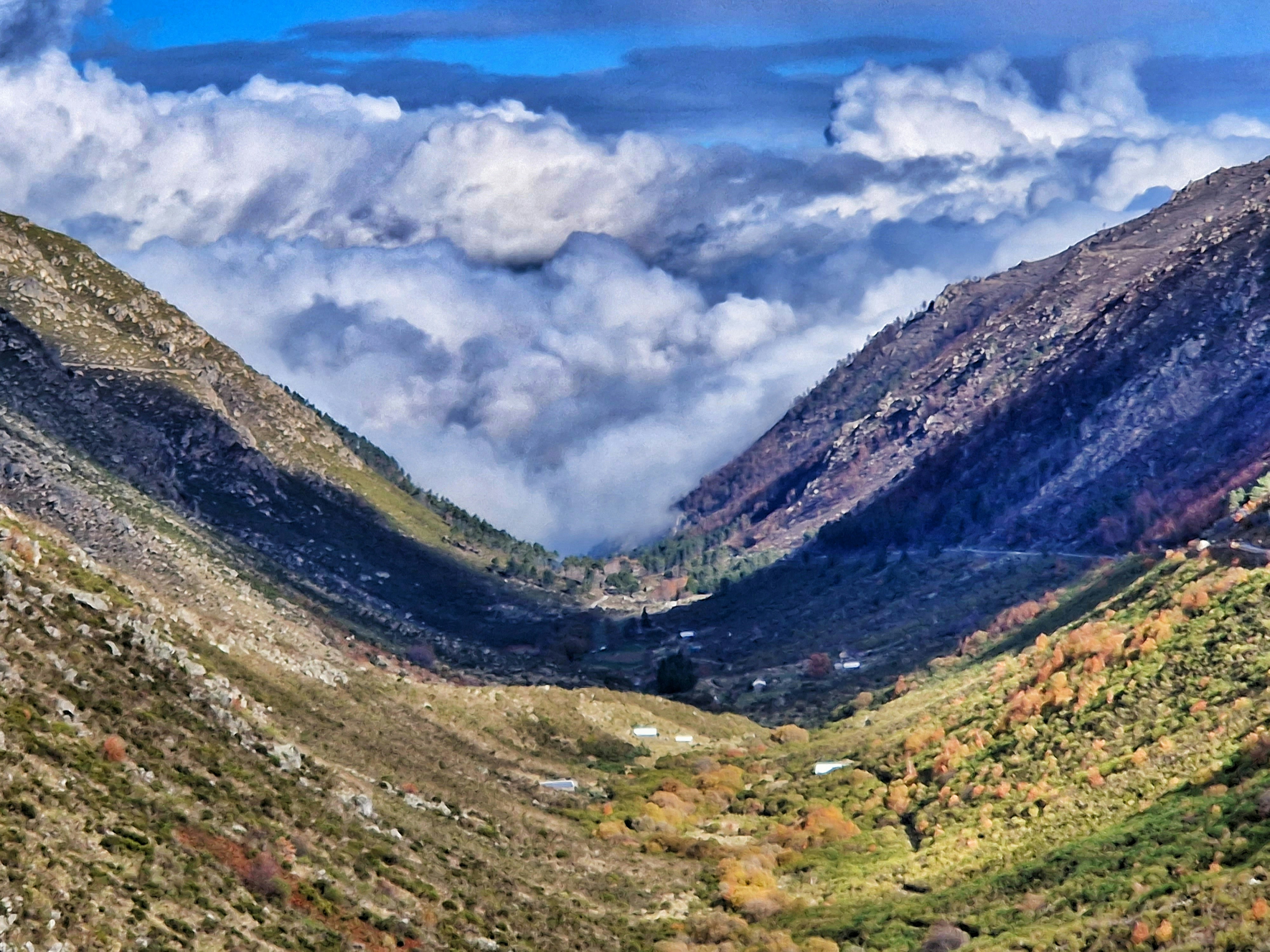 Lush green valley cradled between rugged mountains with clouds spilling over the peaks.