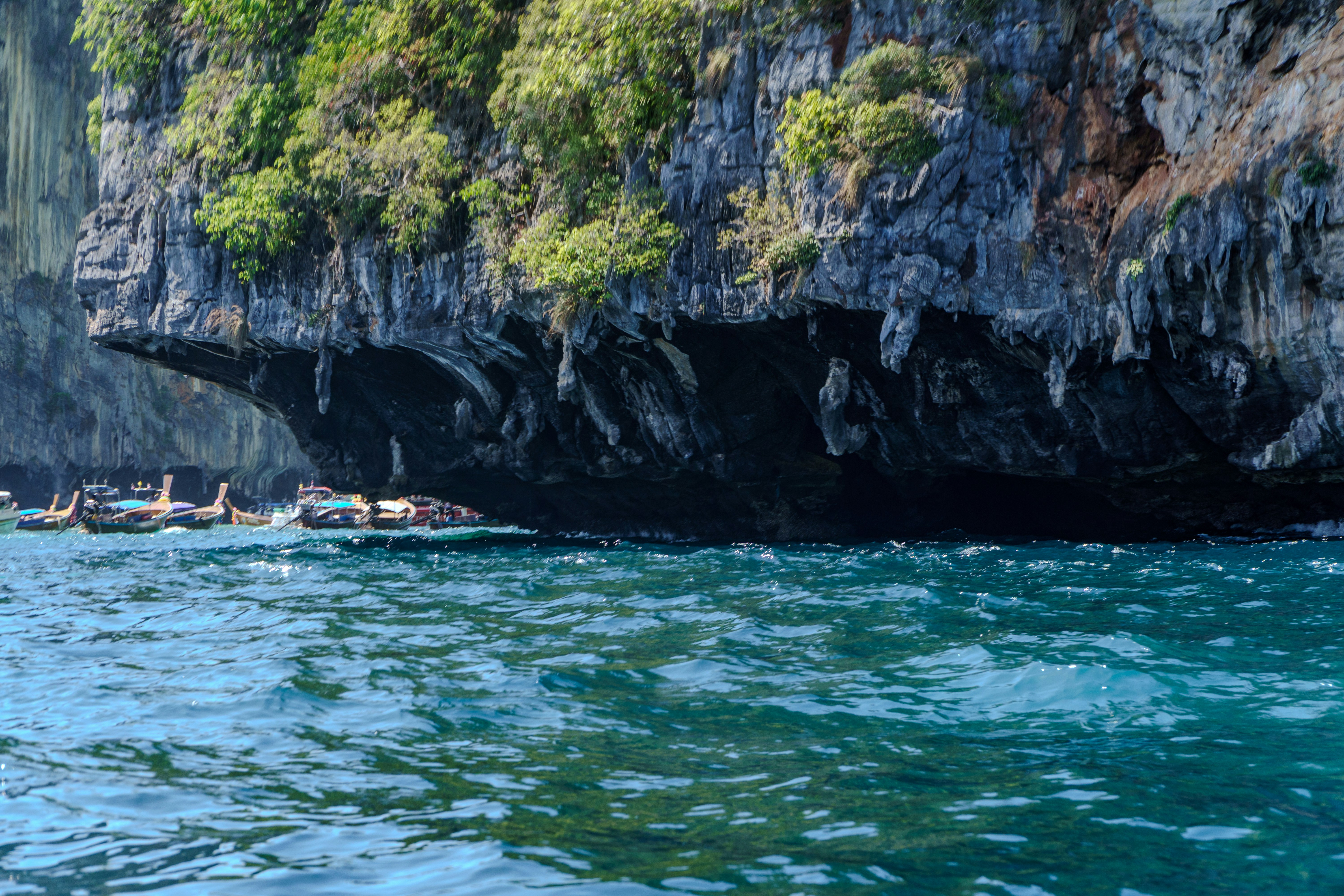 A cliffside overhangs the beautiful, blue ocean water. photo – Free ...