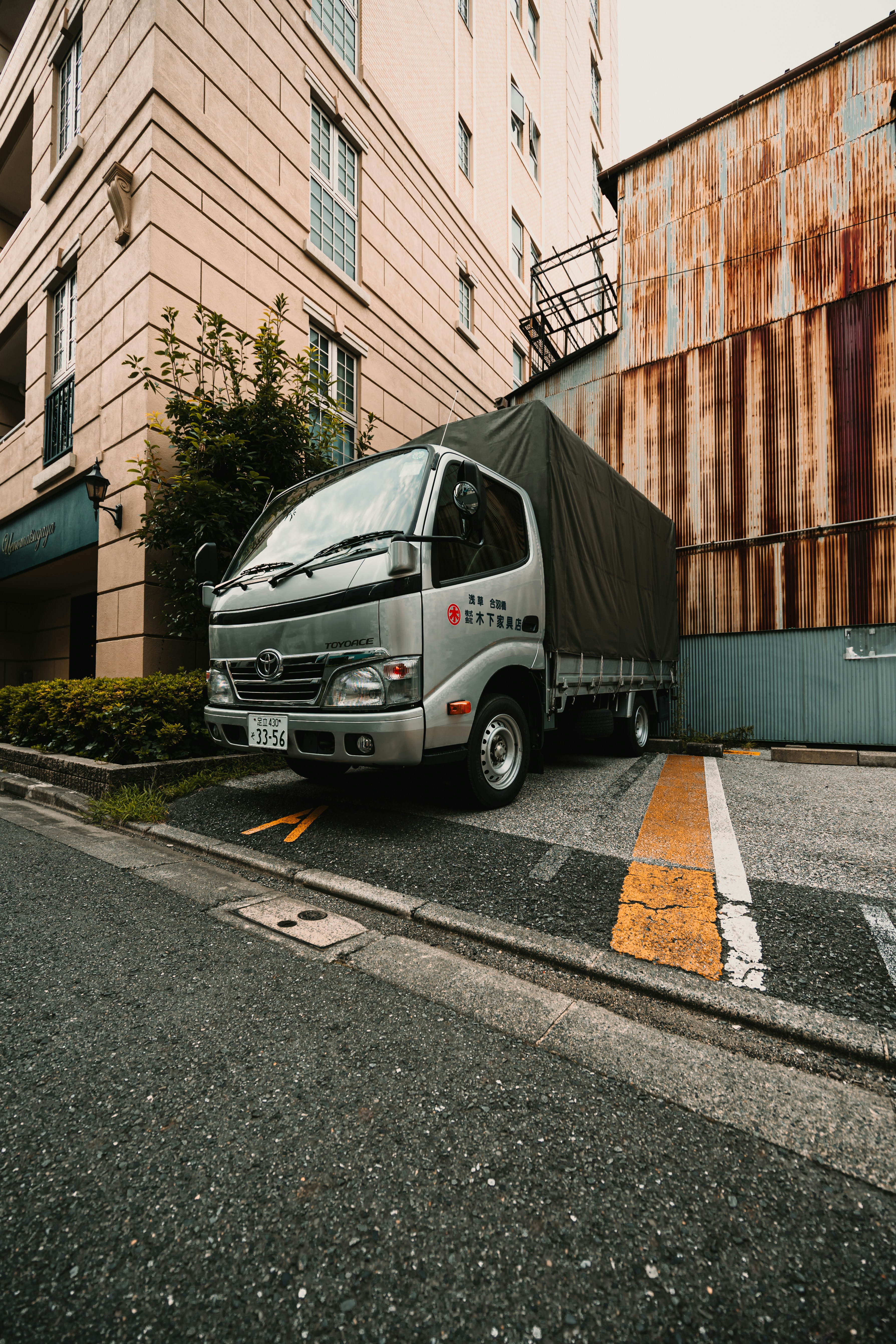 Silver Cargo Truck Nestled Between Beige Facades and a Rusted Warehouse