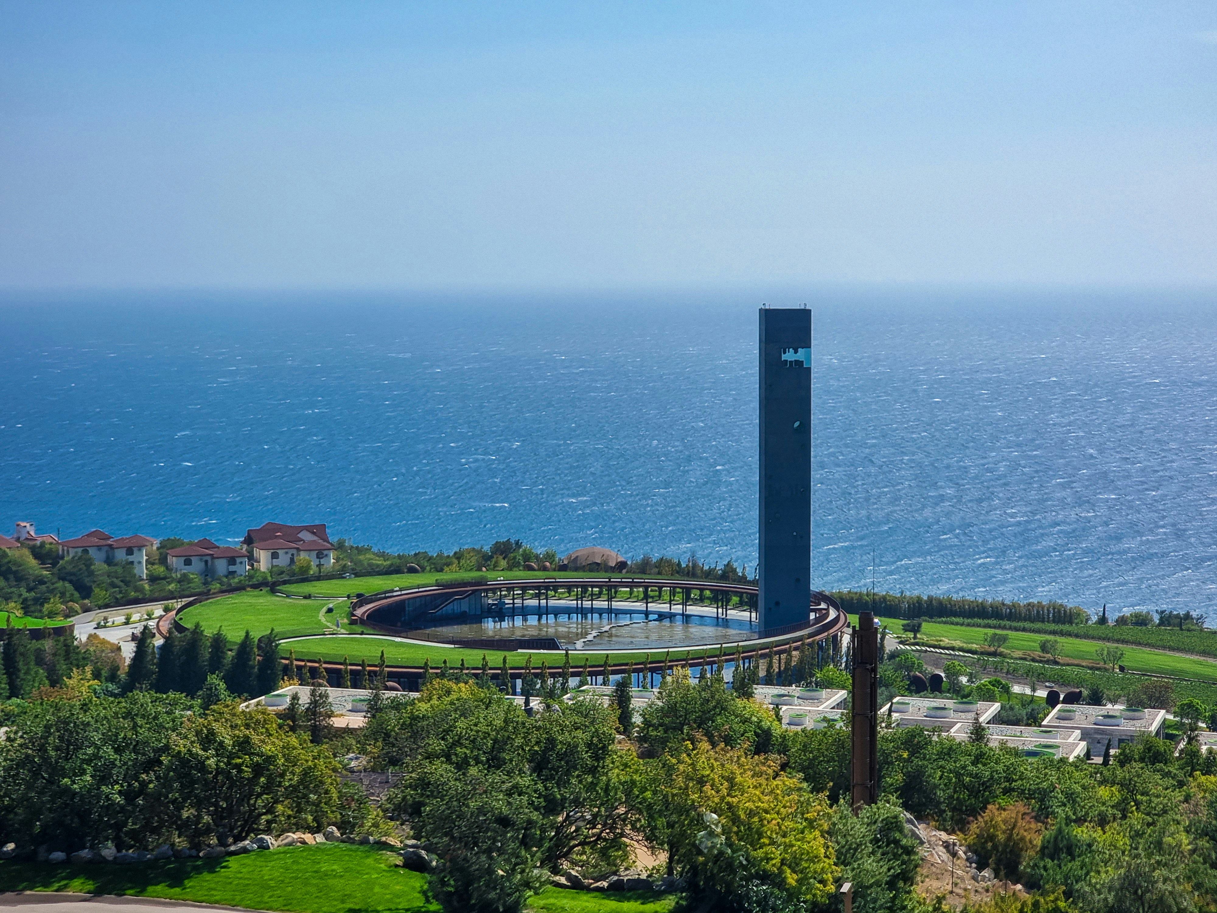 Tall black tower amidst lush greenery overlooking a vast blue sea under a clear sky.