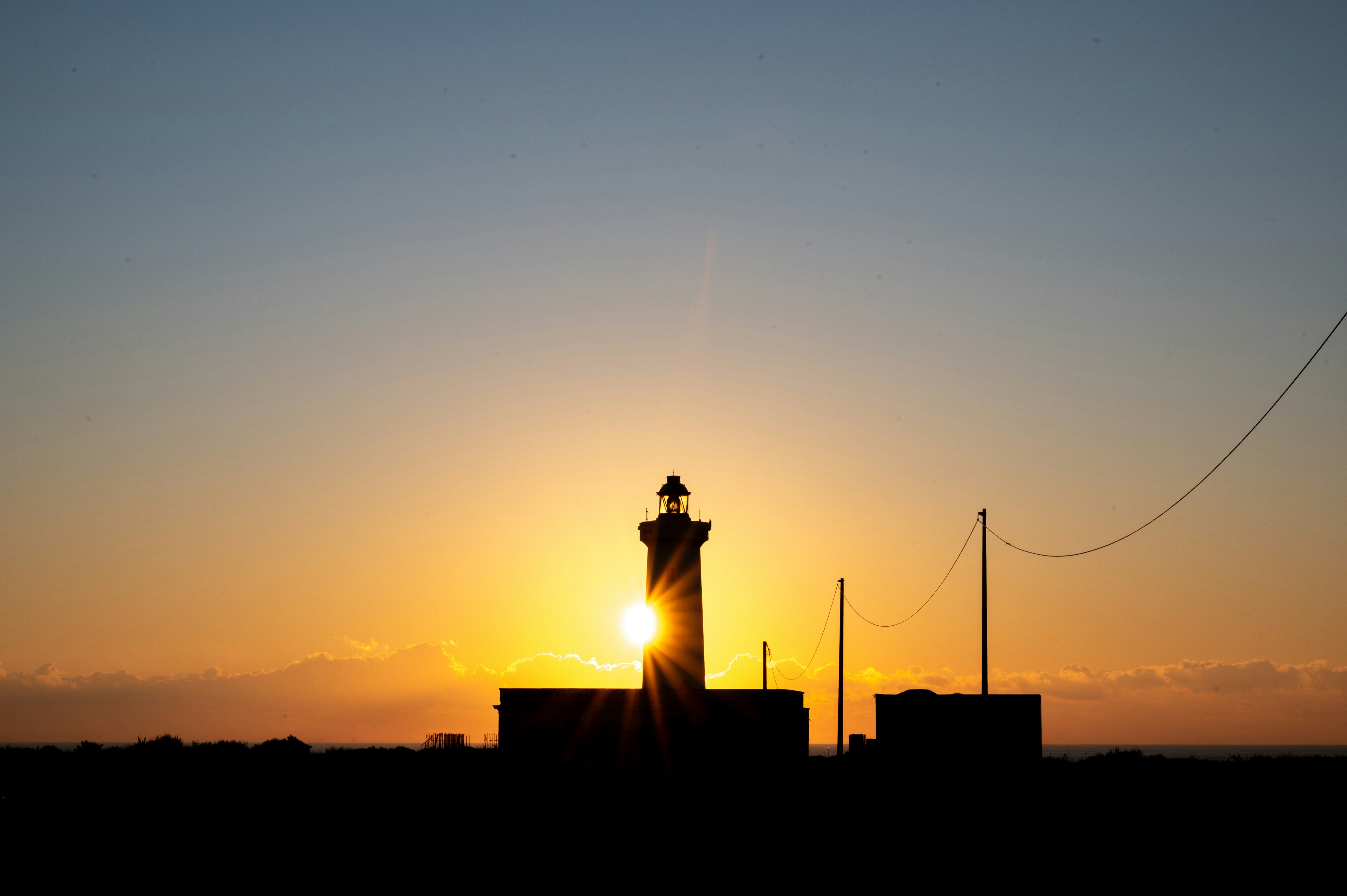 Silhouette of a lighthouse against a vibrant sunrise sky.