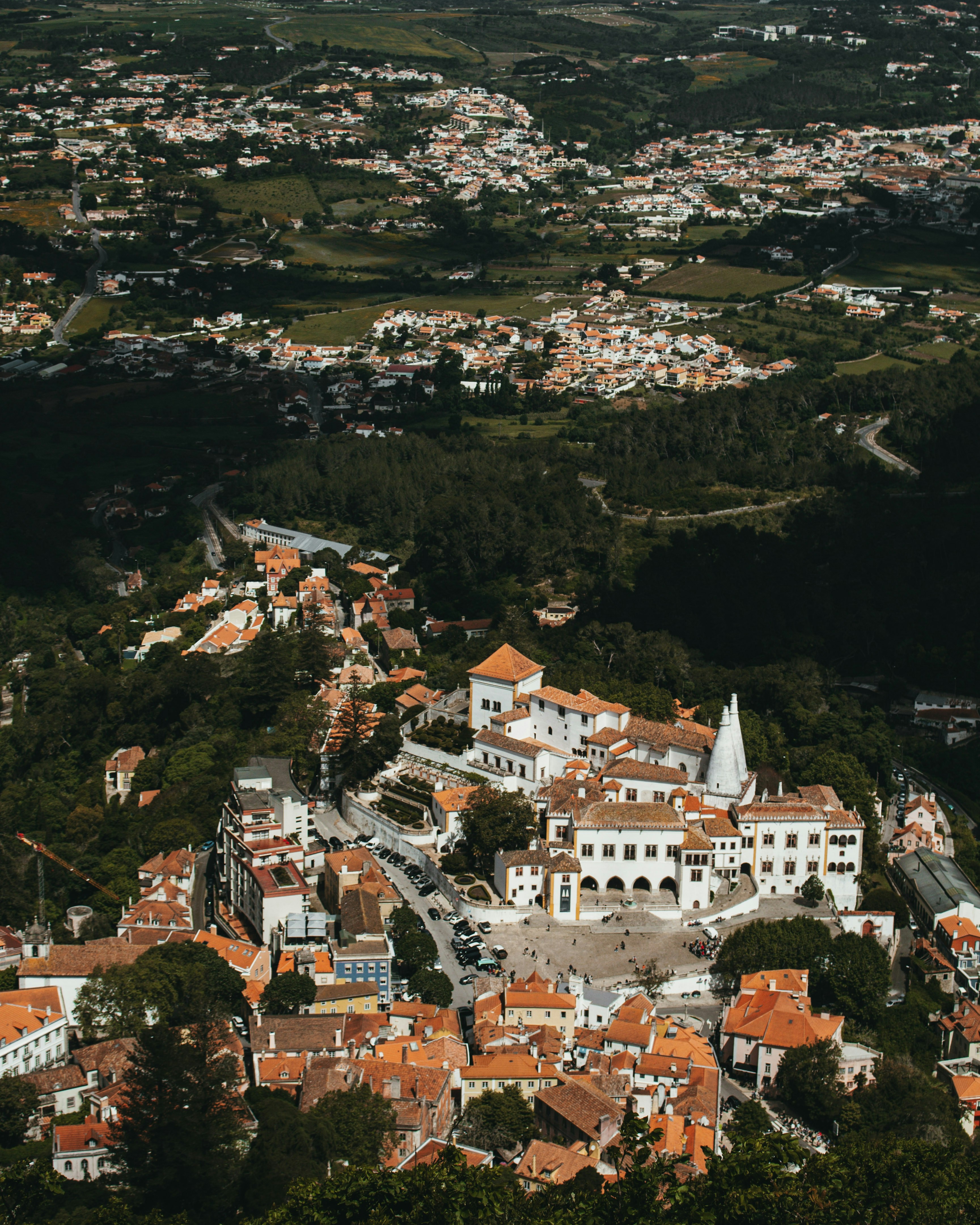 Historic town center of Sintra nestled among lush greenery, showcasing traditional architecture and vibrant orange rooftops.