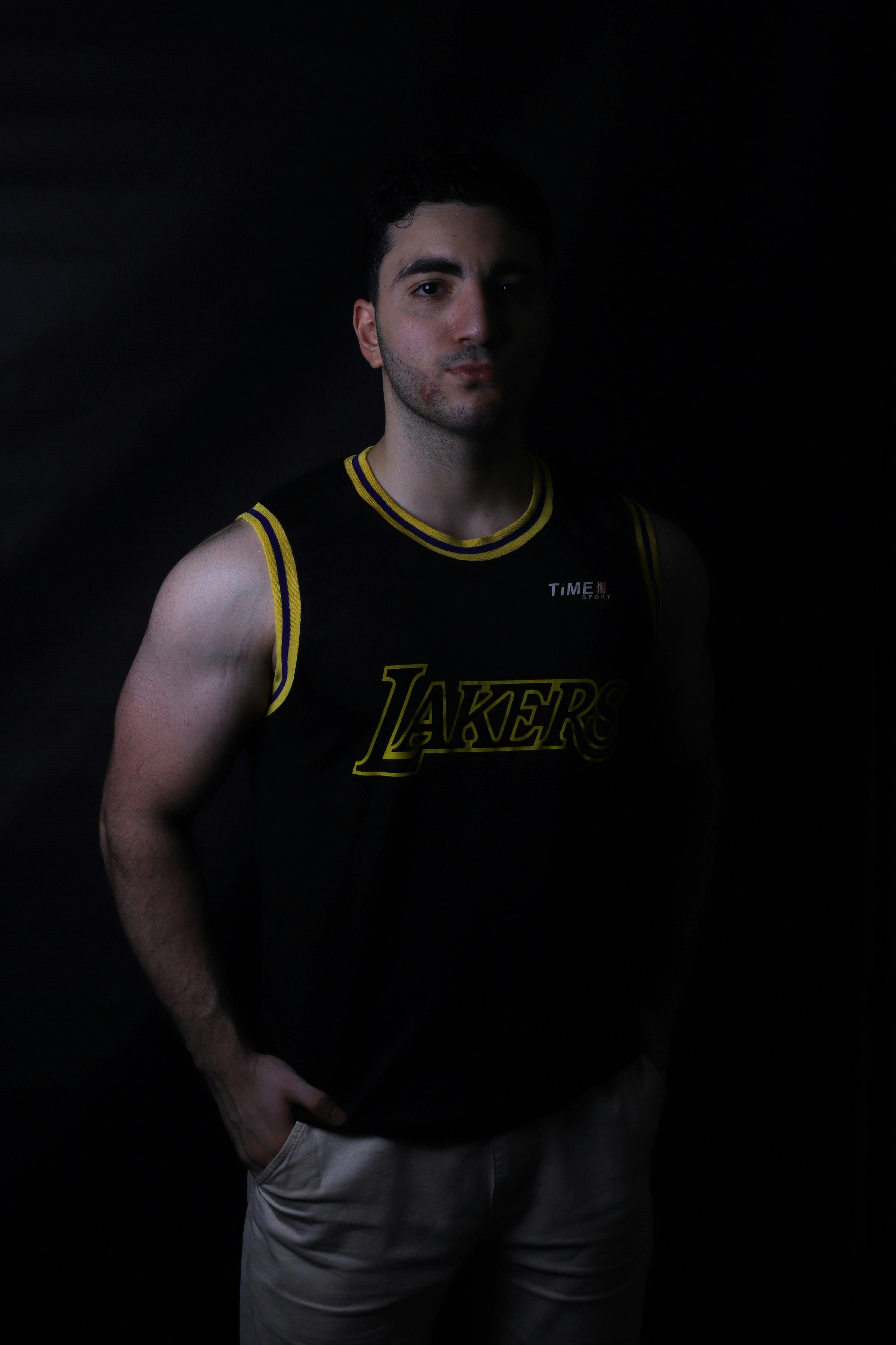 A young man in a Lakers jersey stands confidently against a dark backdrop, showcasing a blend of athleticism and poise.