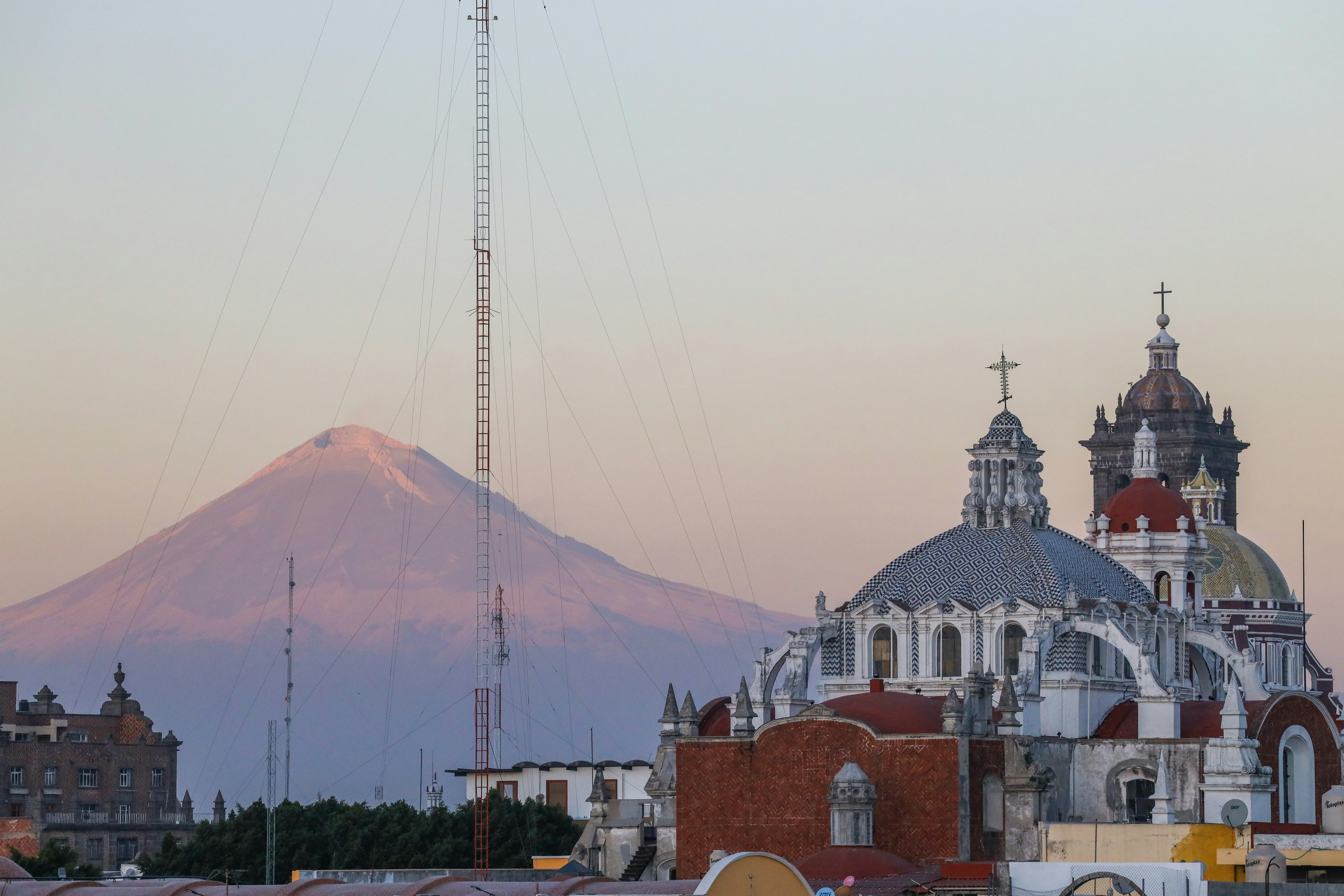 Popocatépetl Volcano at sunrise, framed by Puebla's historic architecture and a towering antenna.
