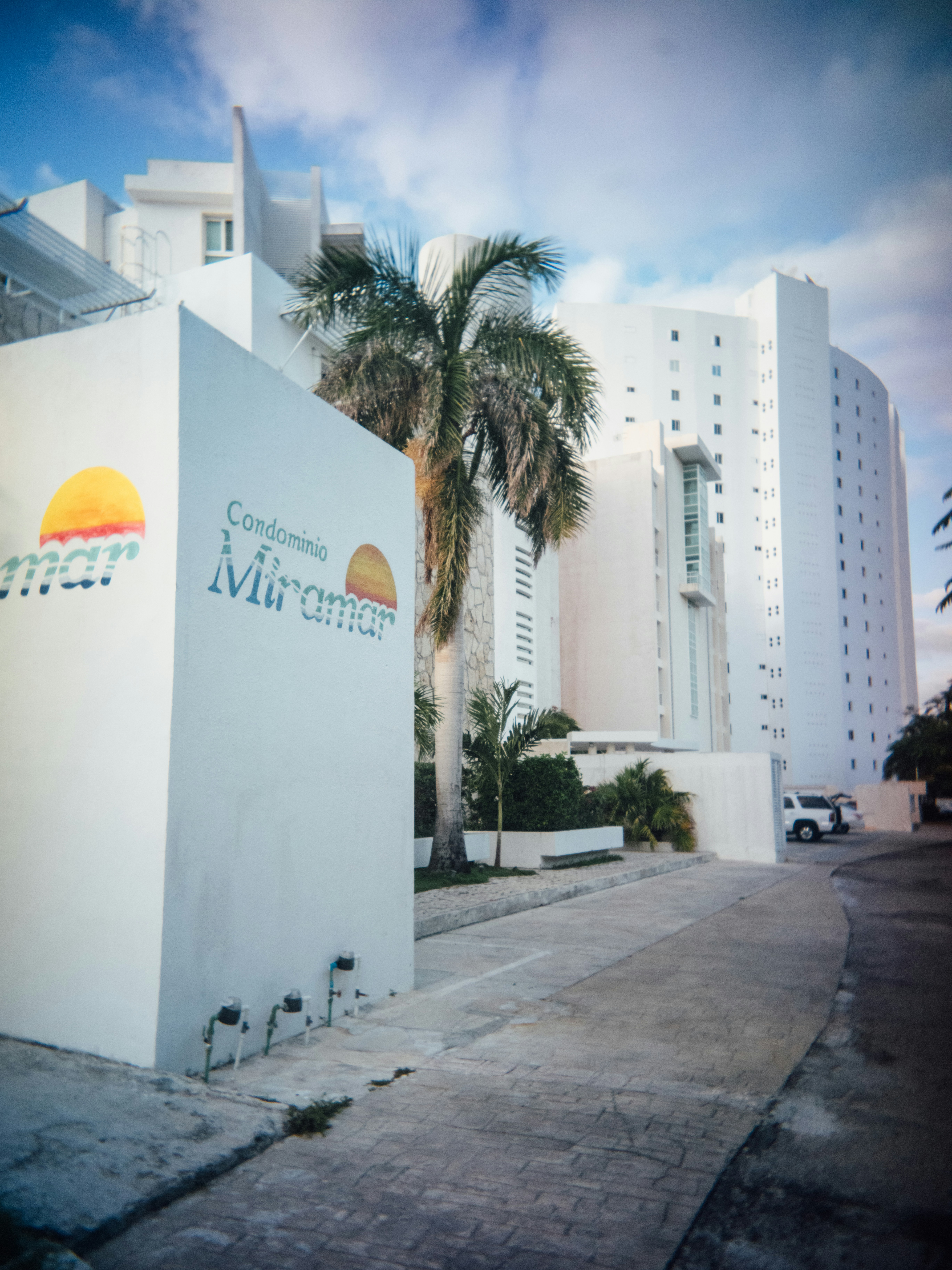 White high-rise building with palm trees under a partly cloudy sky.