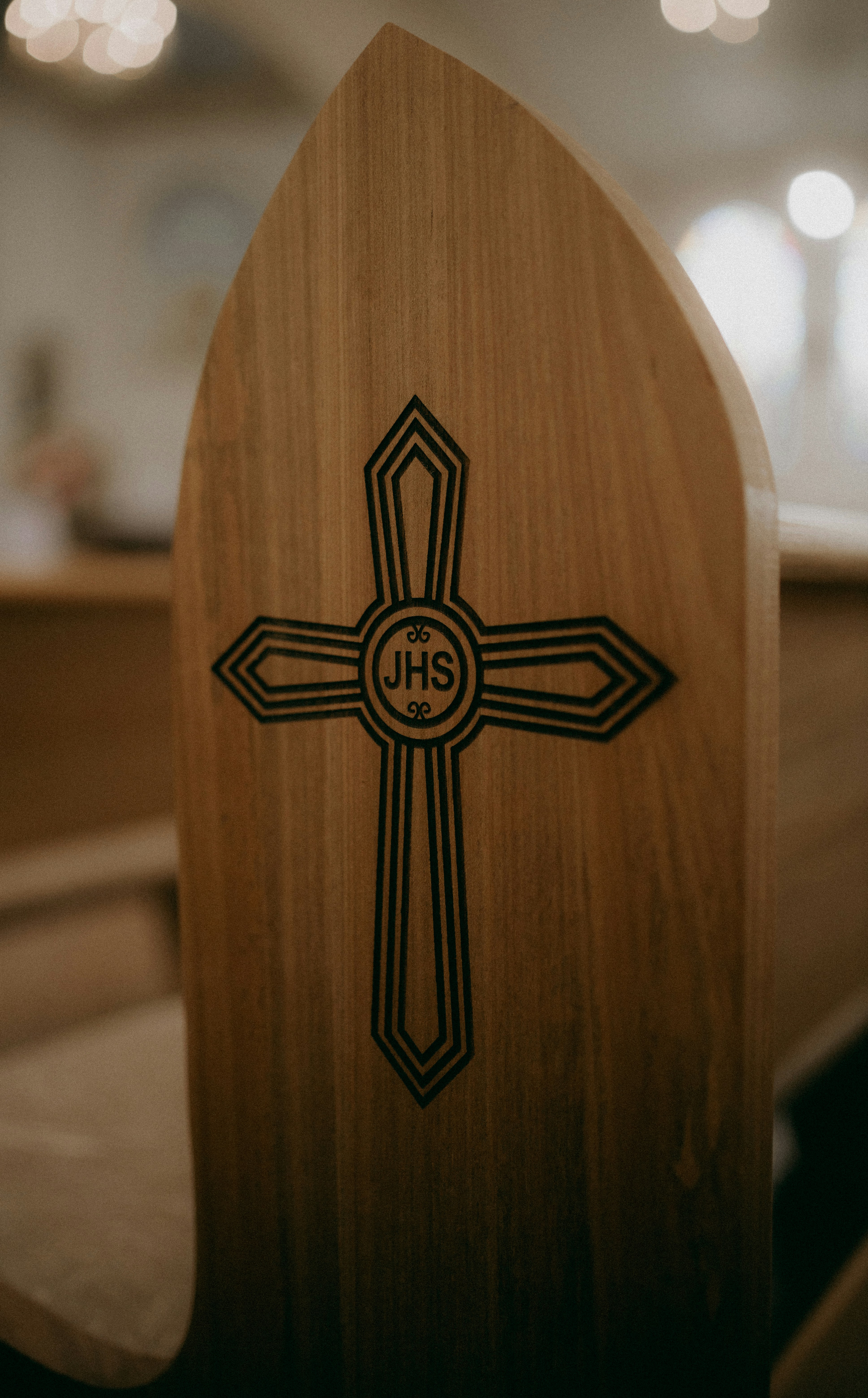 JHS Cross Carved in Warm Wood Under Soft Church Lighting