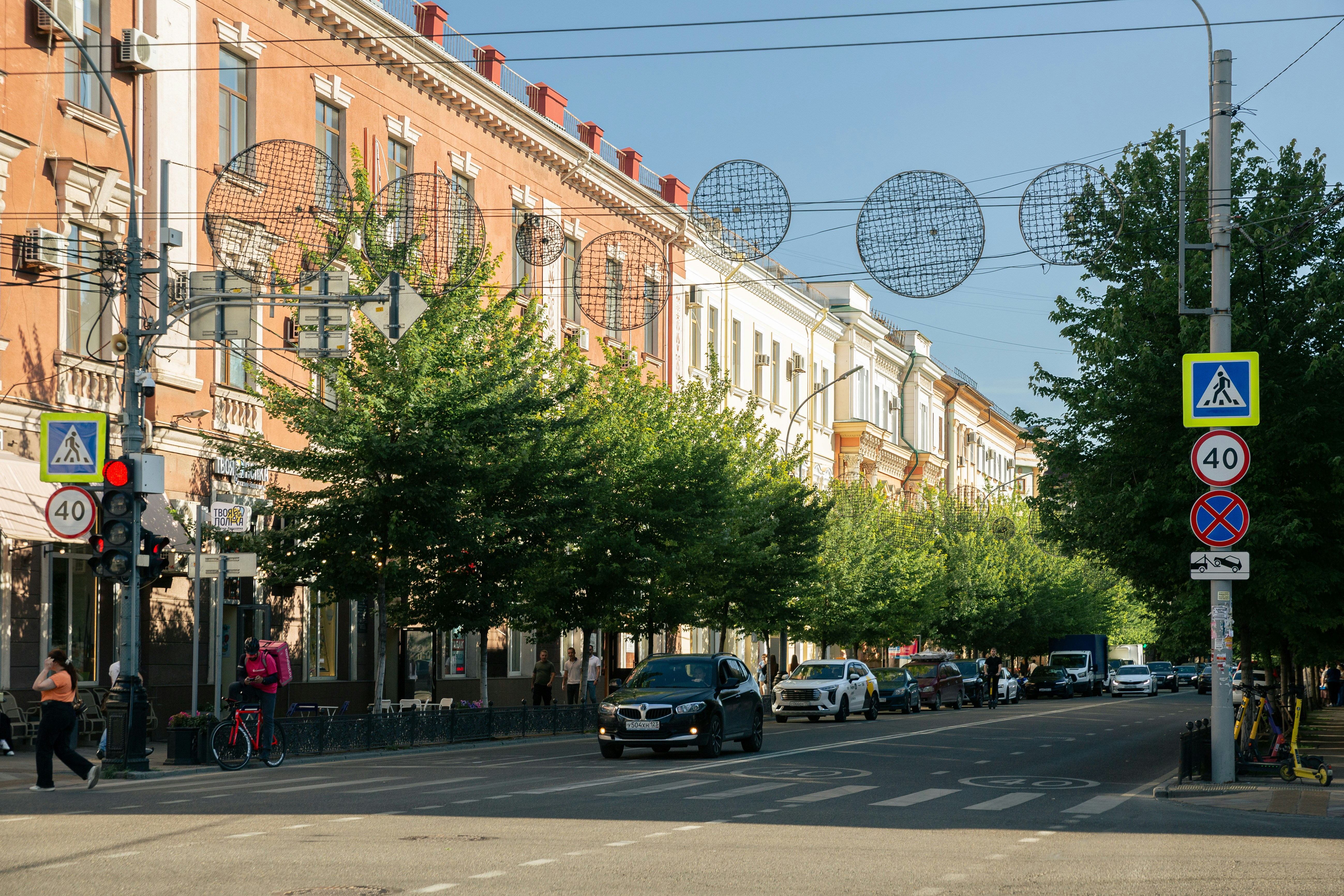 Sunlit Boulevard: Trees, Pedestrians, and Pastel Facades in Motion