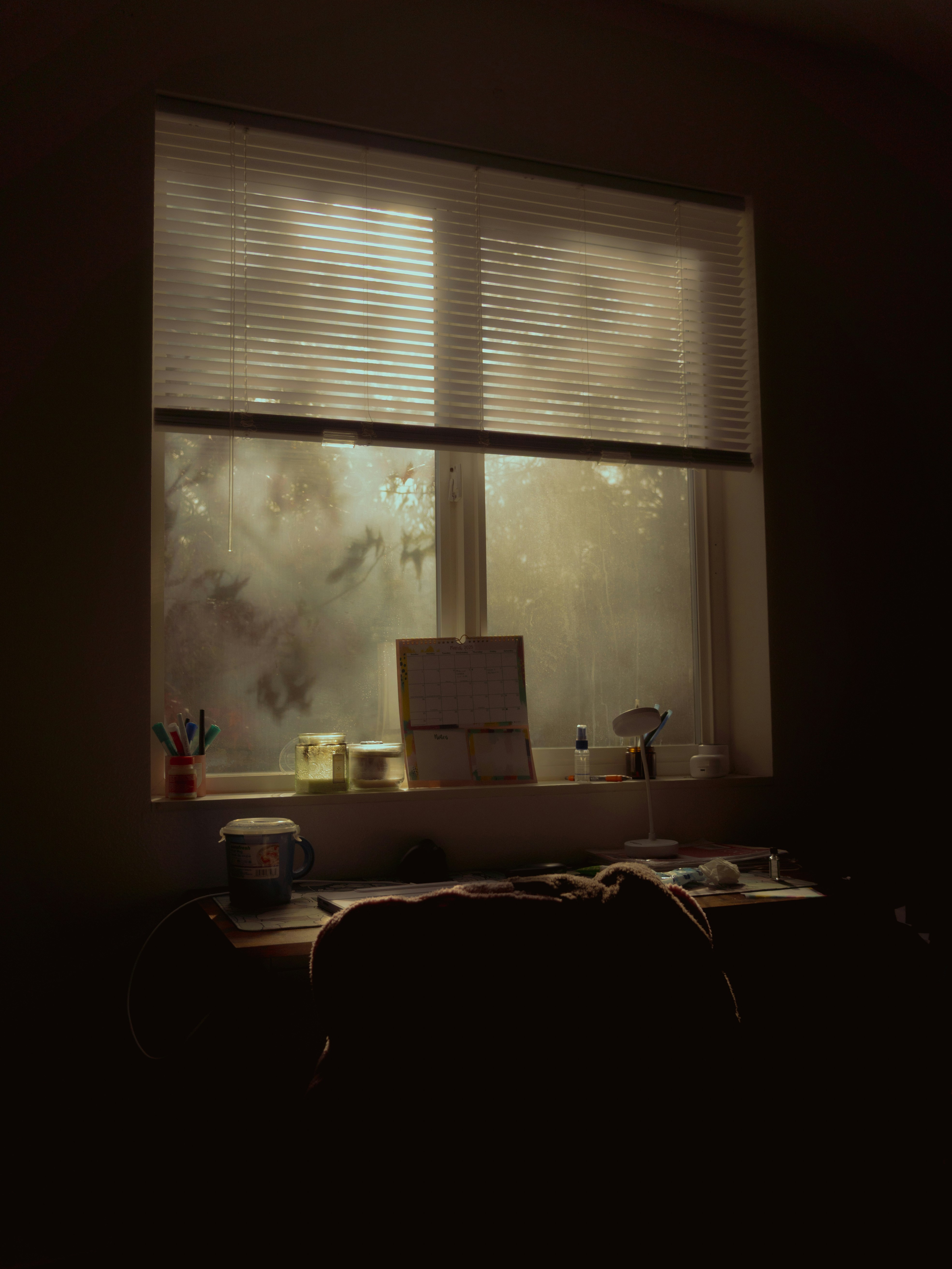 Sunlight filters through a fogged window, illuminating a workspace filled with everyday objects and soft shadows.